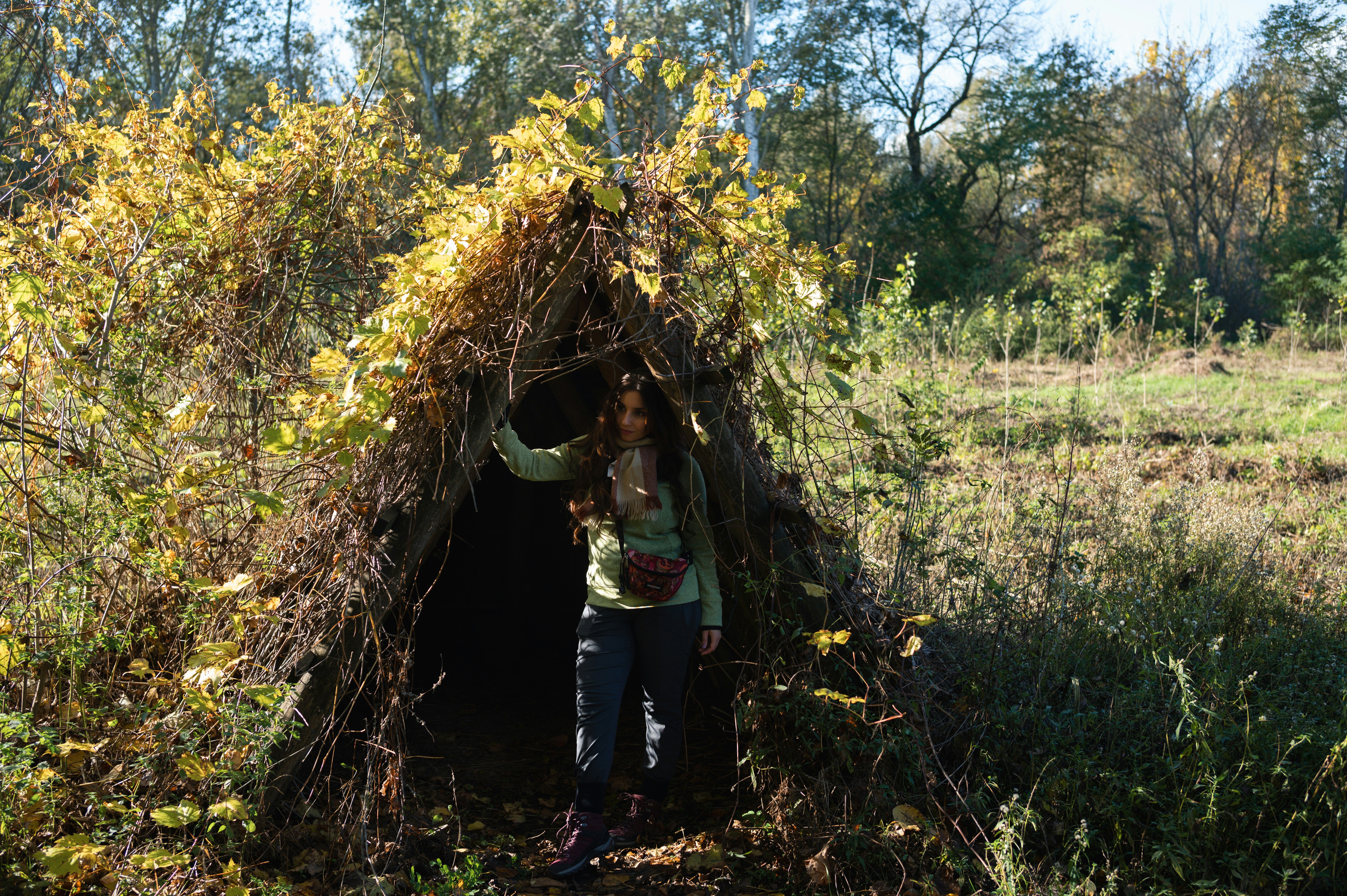 Child Emerging from a Leafy Hut in Autumn Field
