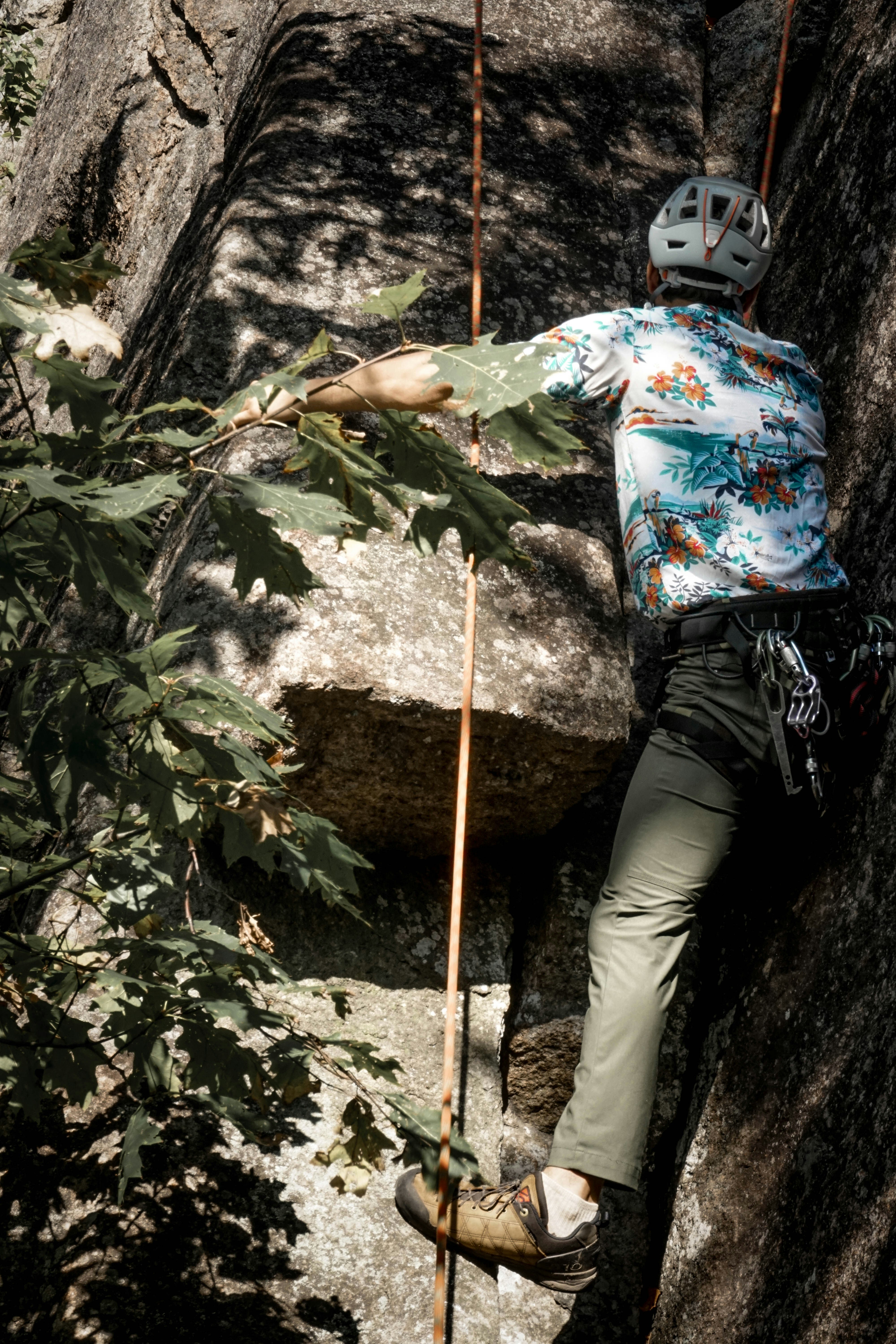 Climber in a floral shirt navigates a rocky ascent, showcasing determination and skill amidst nature. The scene captures the essence of outdoor adventure.