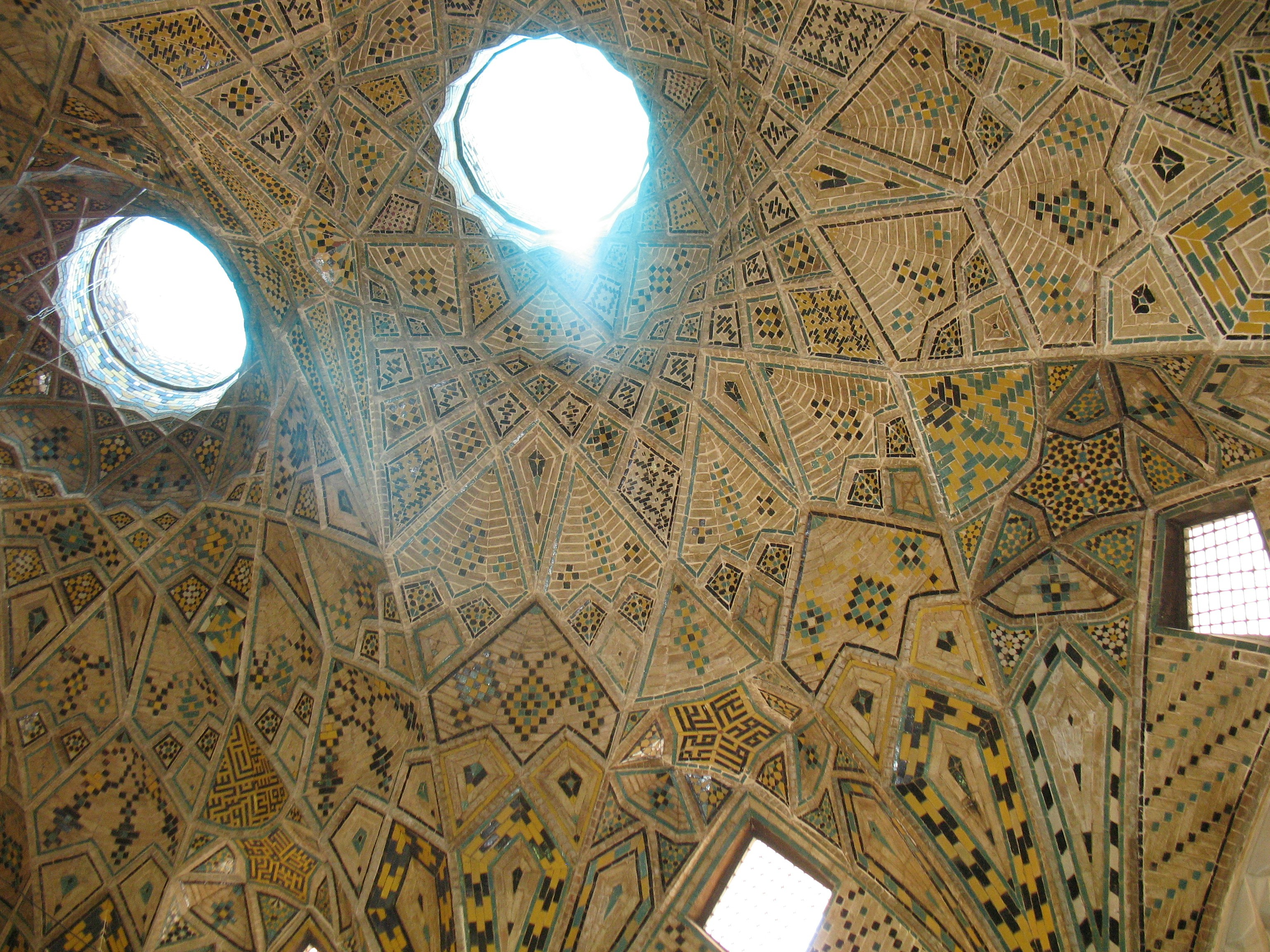 Intricate geometric patterns and vibrant colors adorn the ceiling, illuminated by natural light streaming through circular openings.