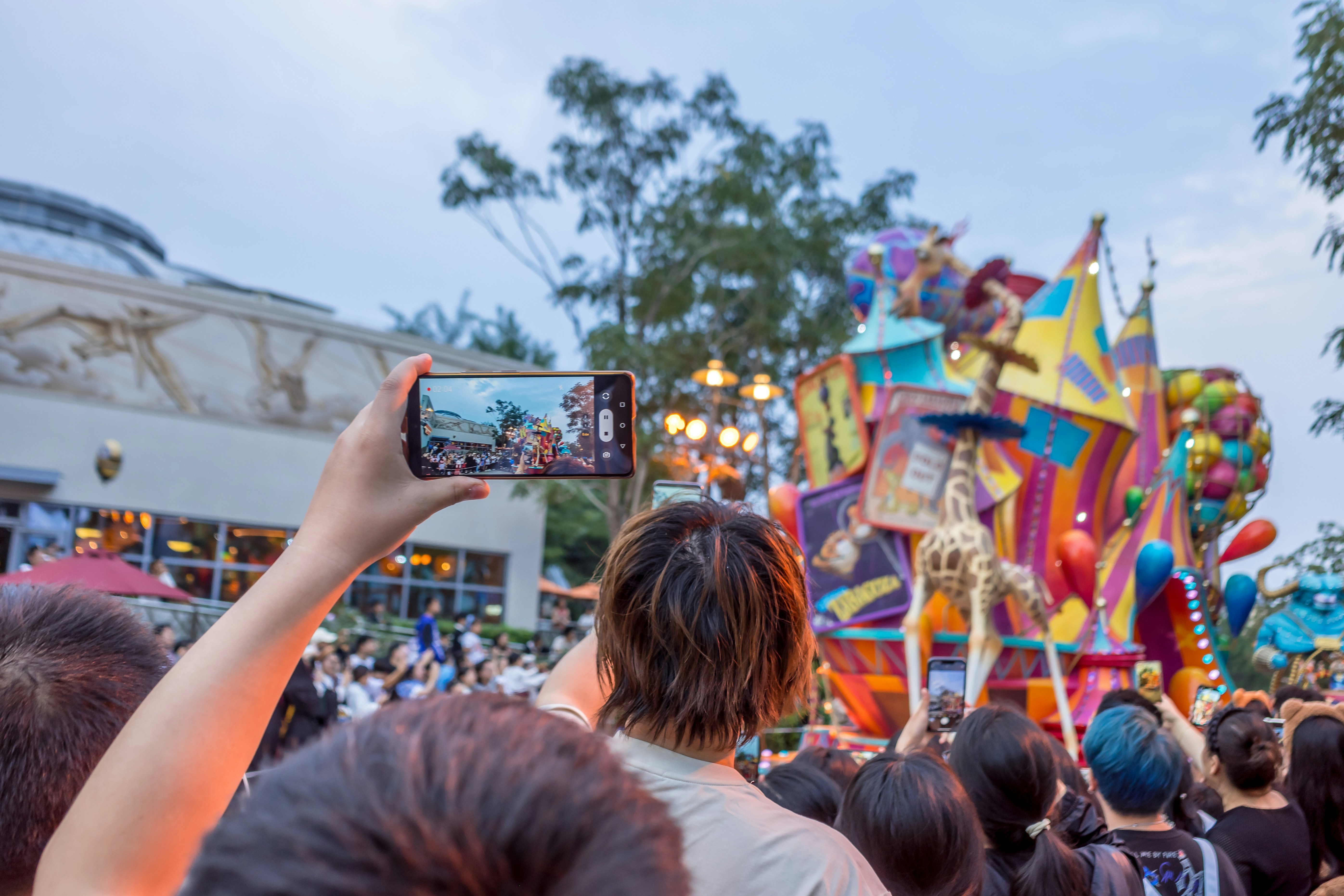 Neon Parade Framed by a Smartphone: A Giraffe Float Among the Crowd
