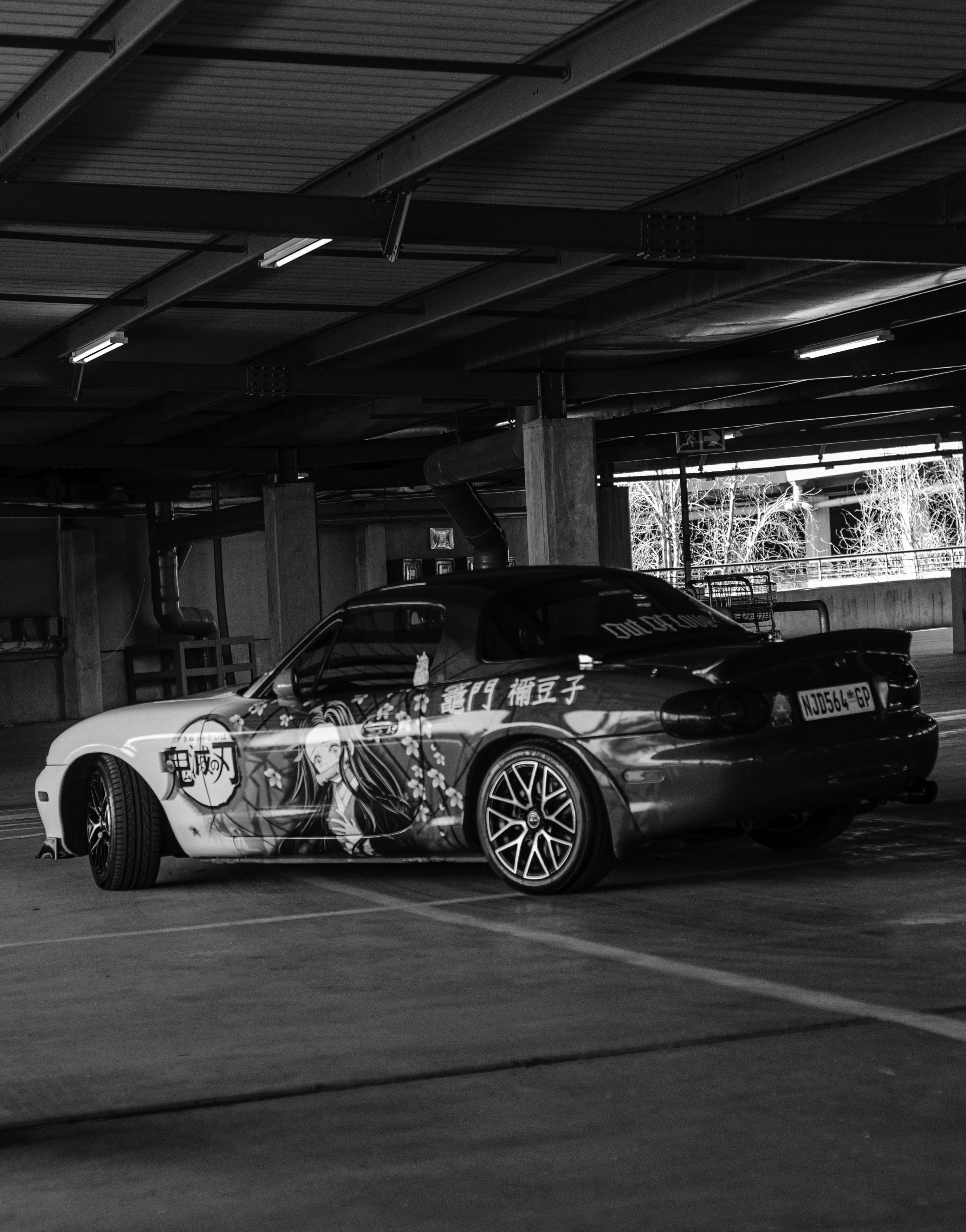 Floral-wrapped sports sedan rests beneath industrial lighting in a dim parking garage