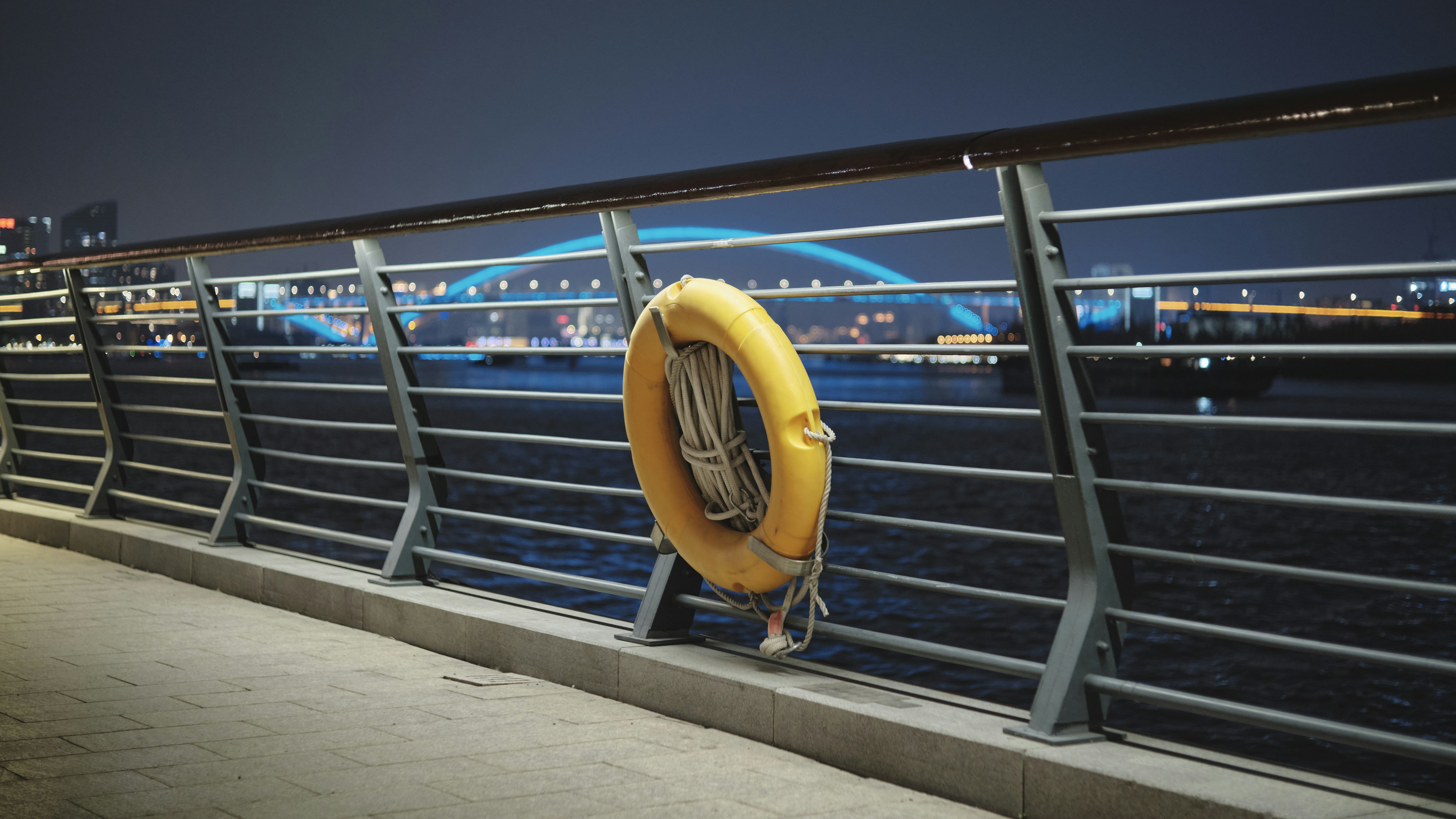 Lifebuoy on a Waterfront Railing Under a Blue-Arch Night Bridge