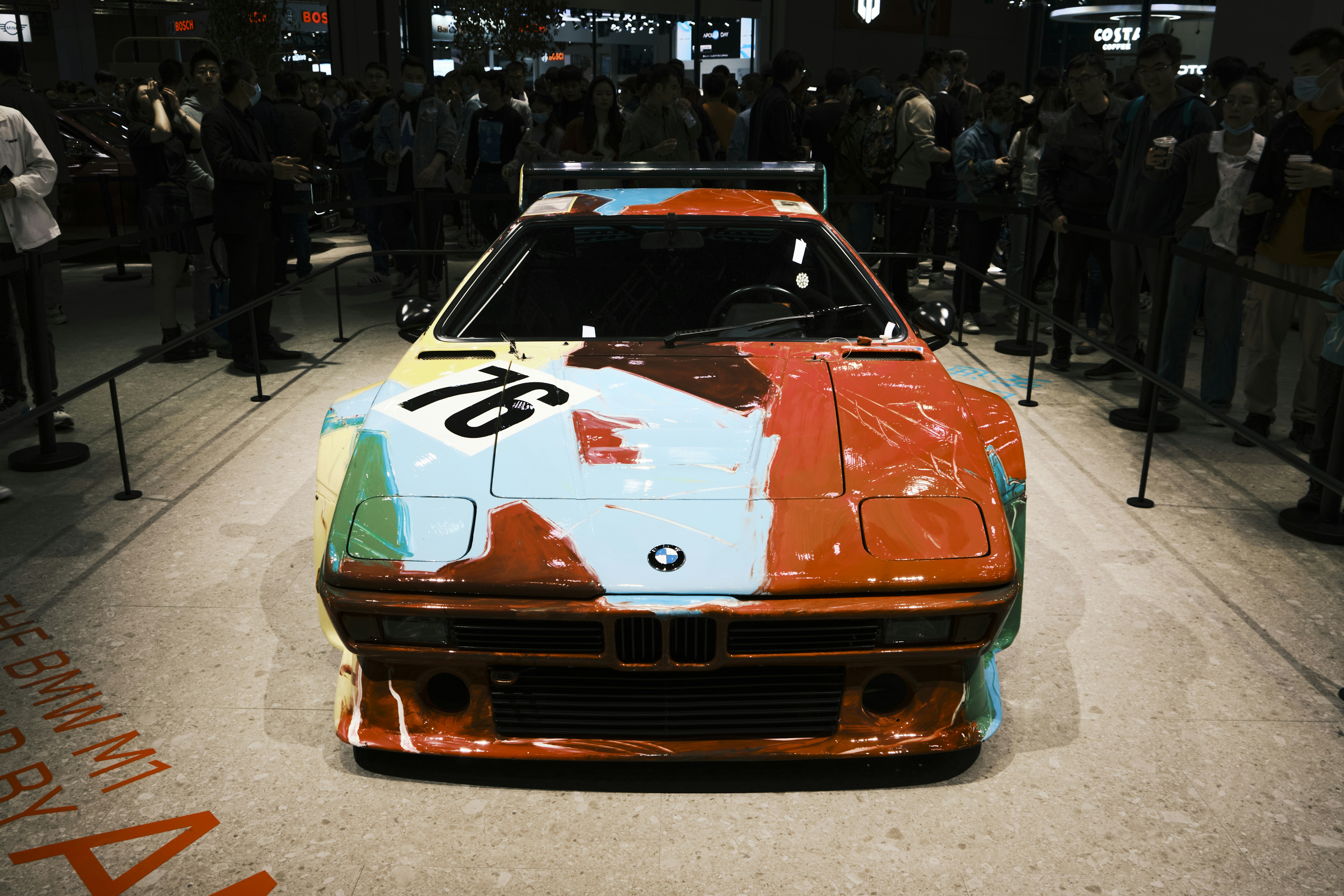 Prismatic Racer on Display: A Color-Wrapped BMW Front Amid Attentive Onlookers