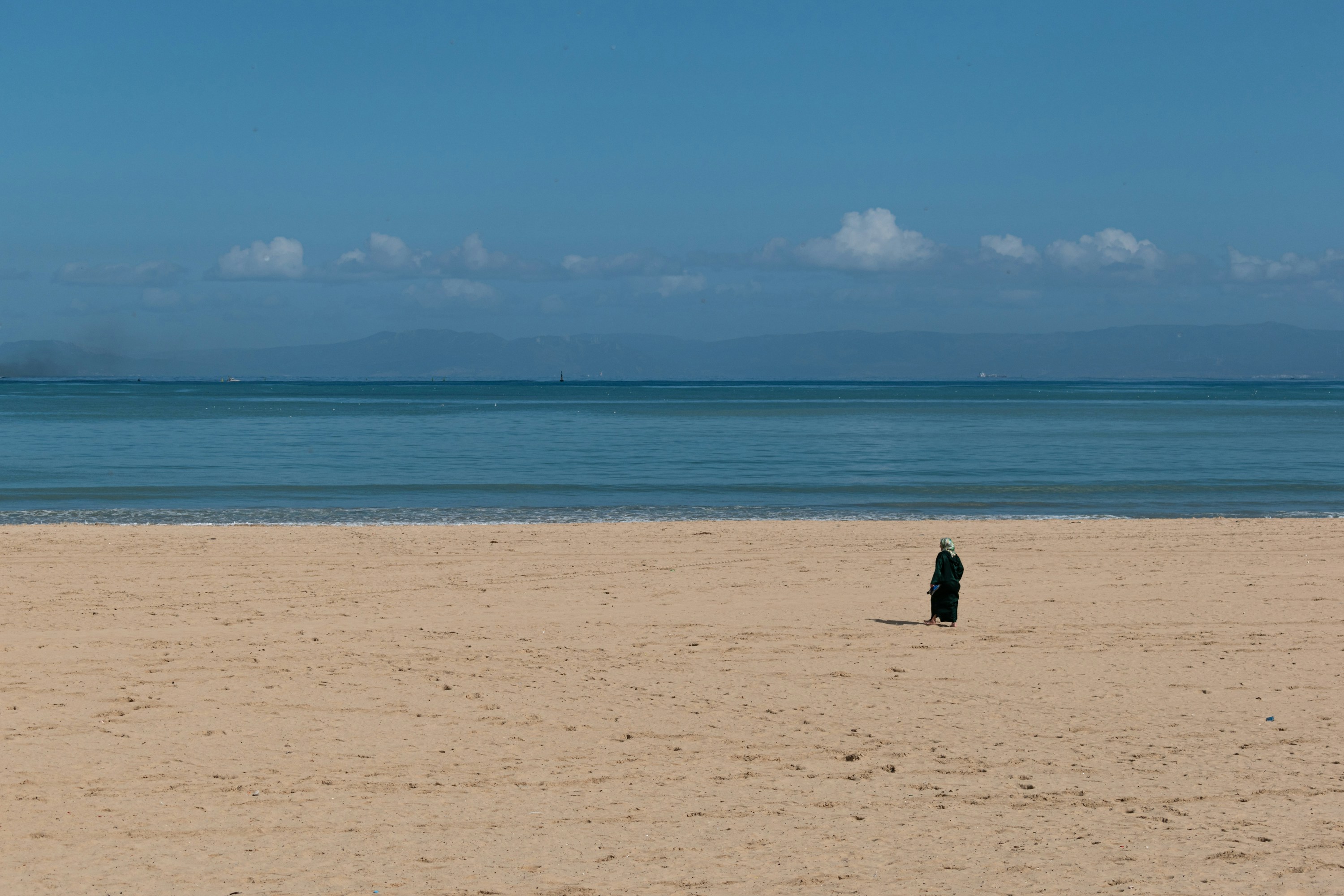 Lone Figure on a Quiet Shore Beneath a Wide Blue Horizon