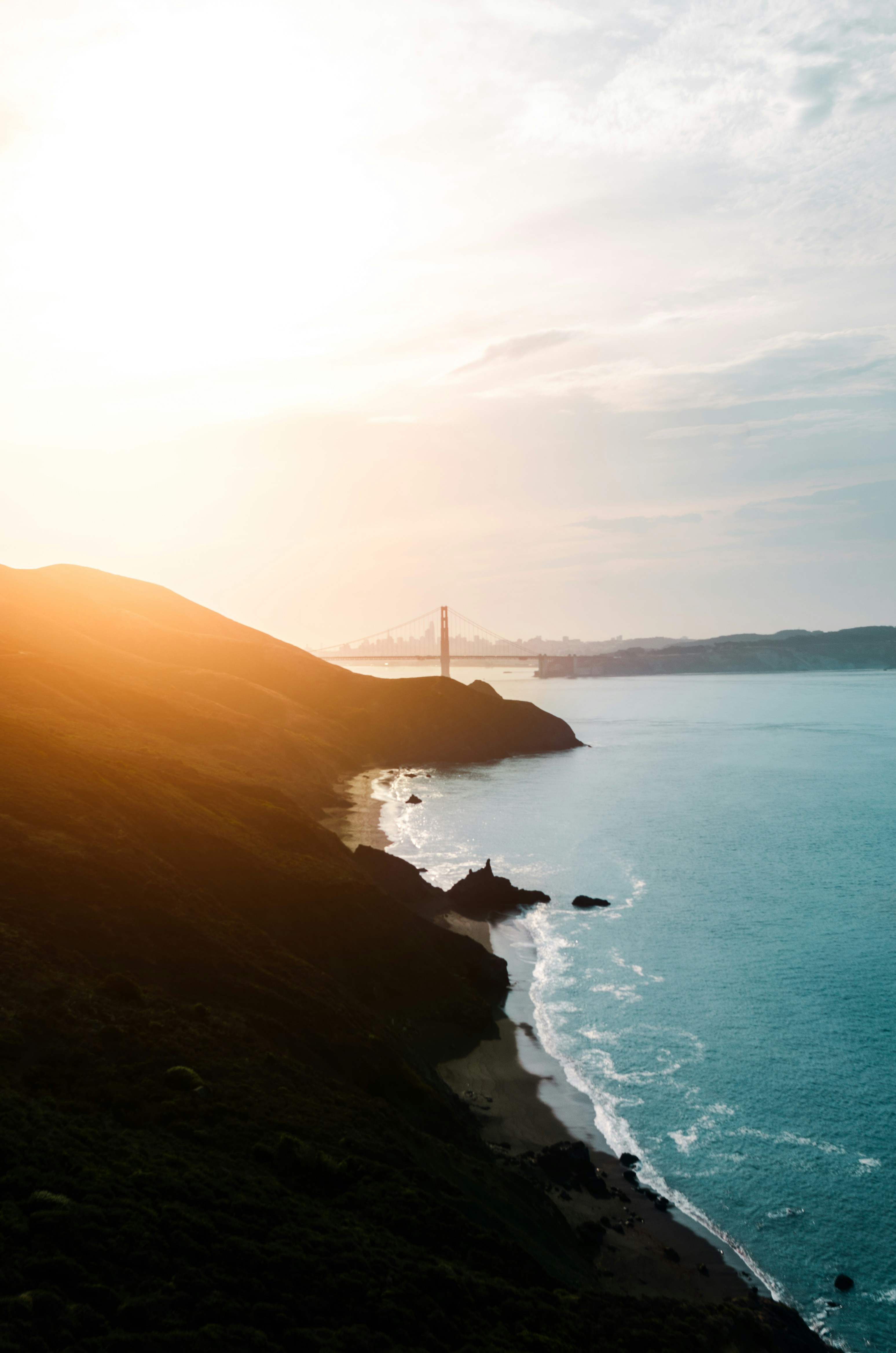 Sunlit Promontory: A Distant Suspension Bridge Emerges Over a Quiet Sea at Dawn