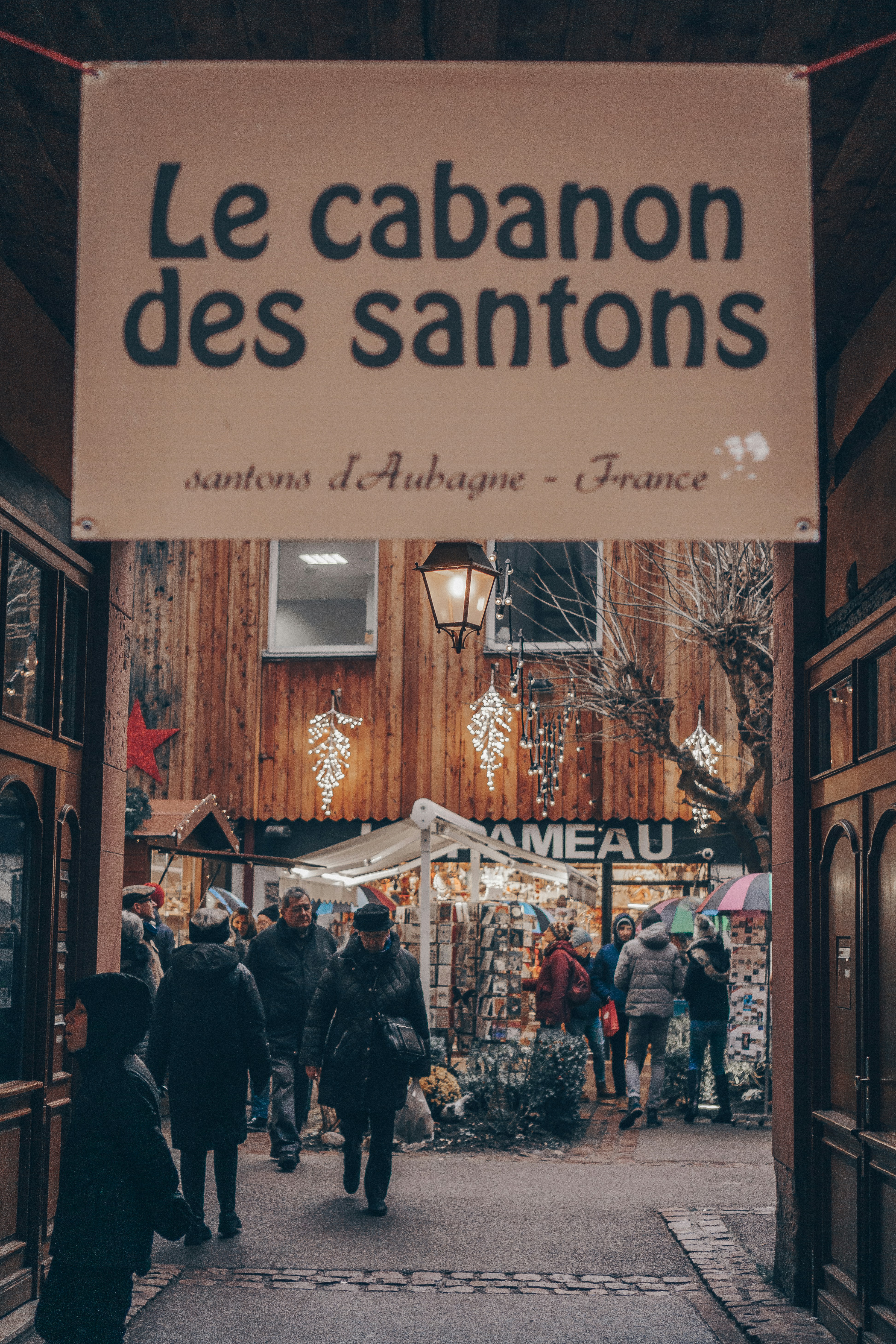 A group of people walking under a sign that says le cabanon des san ...