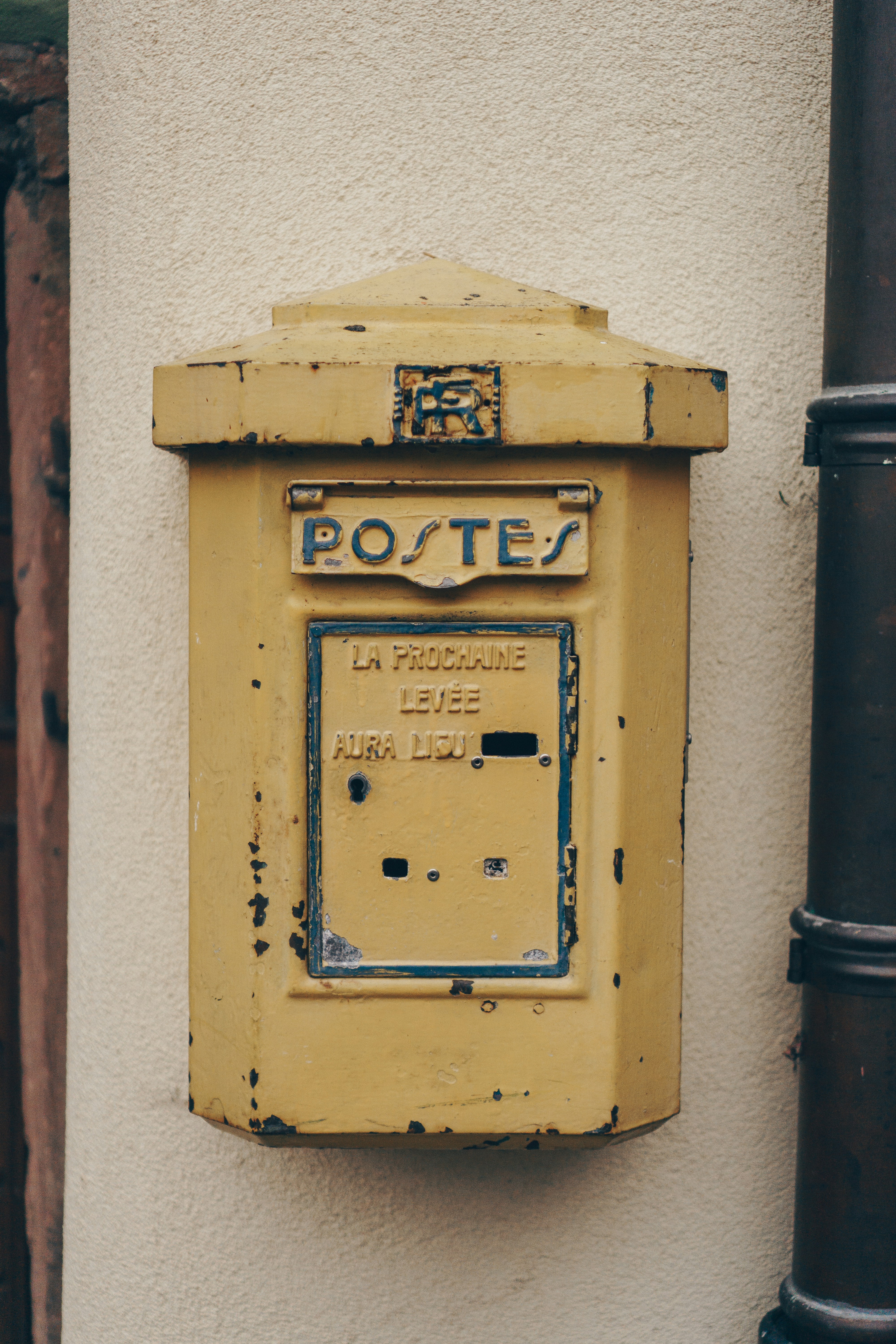 Weathered yellow postal box mounted on a wall, displaying faded text and signs of age. A nostalgic reminder of communication's past.