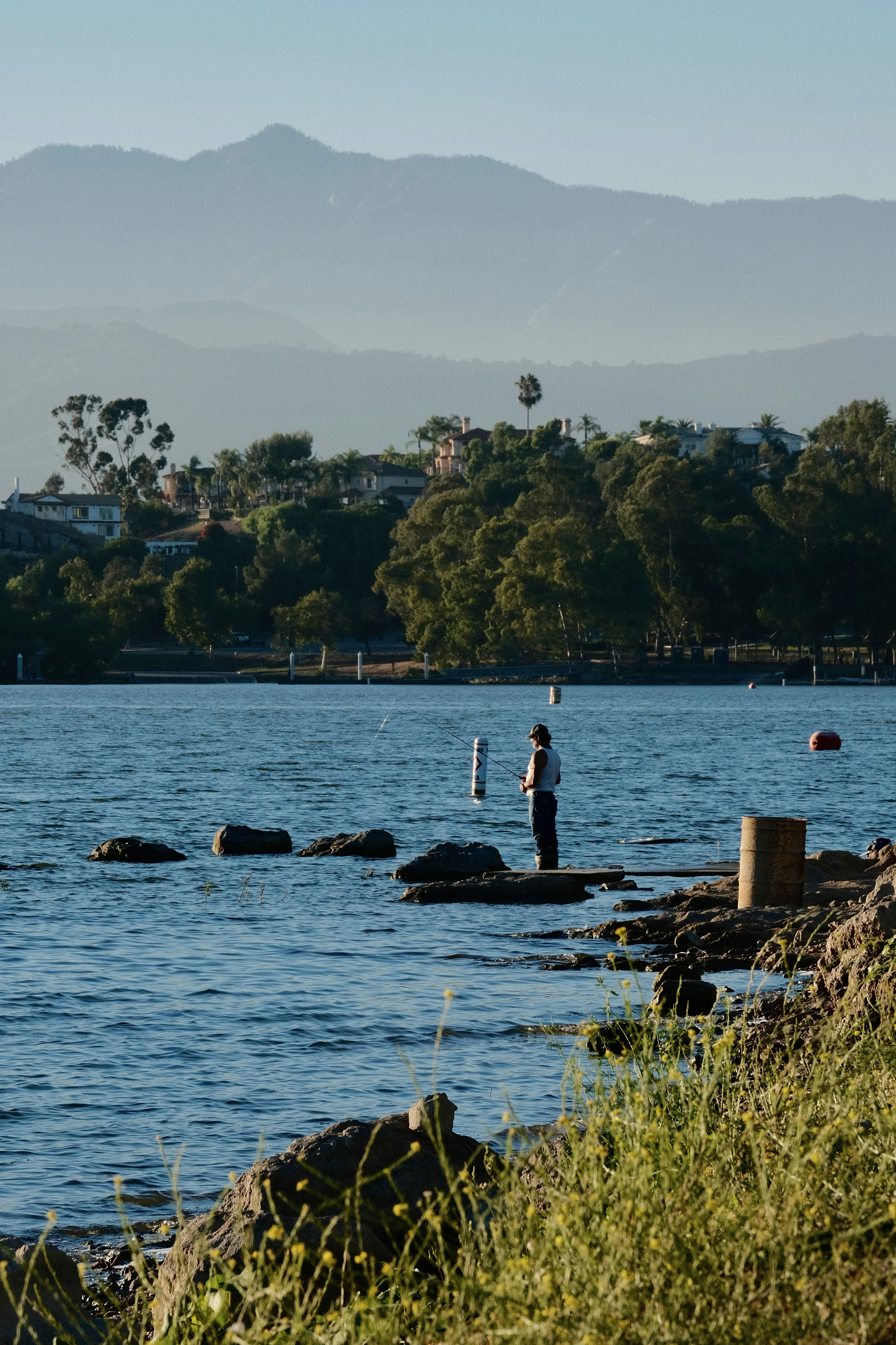 Edge of Quiet: A lone angler at a rocky lakeside as distant mountains loom