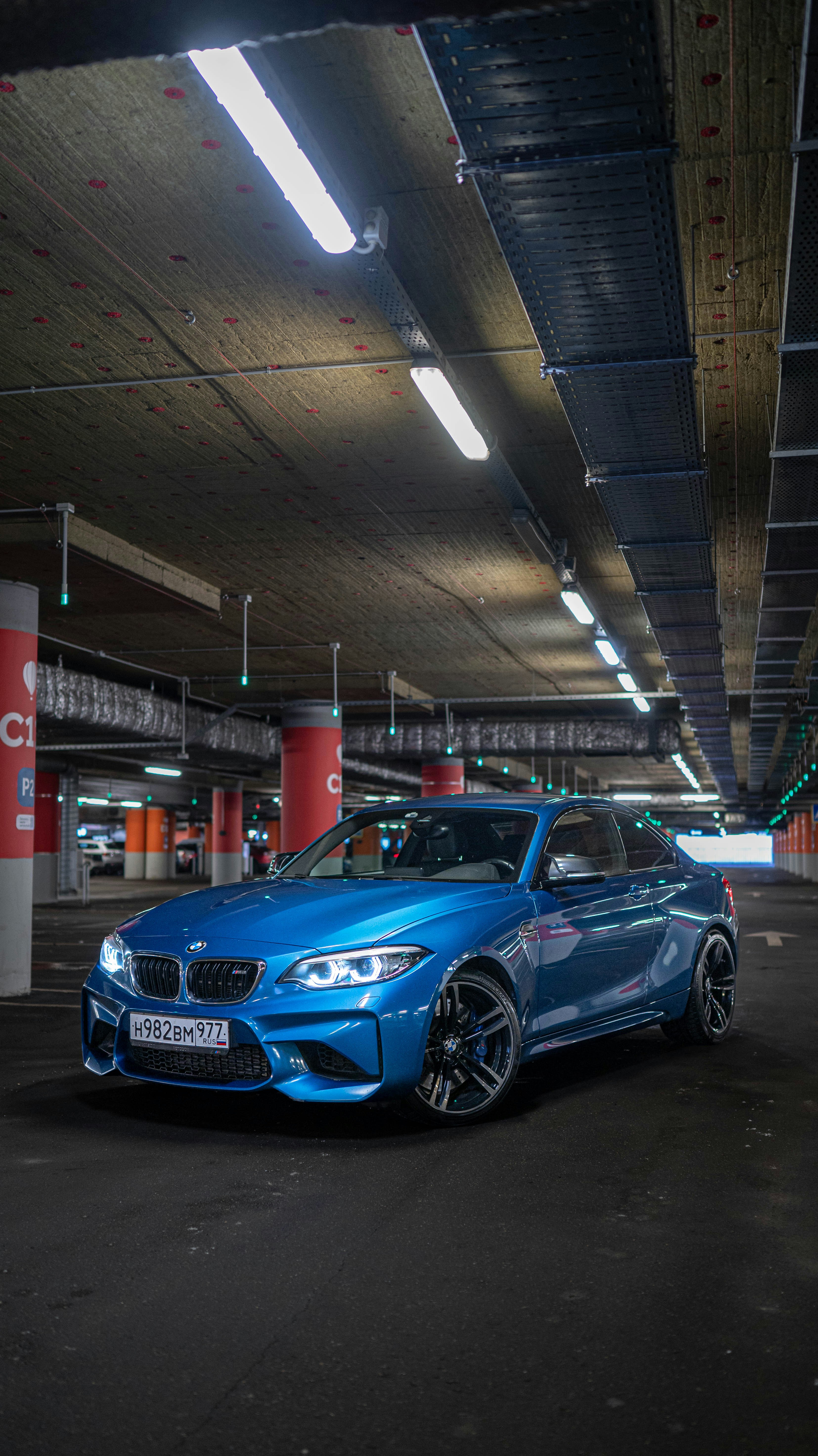 Sleek blue car parked in a dimly lit parking garage with industrial lighting overhead.