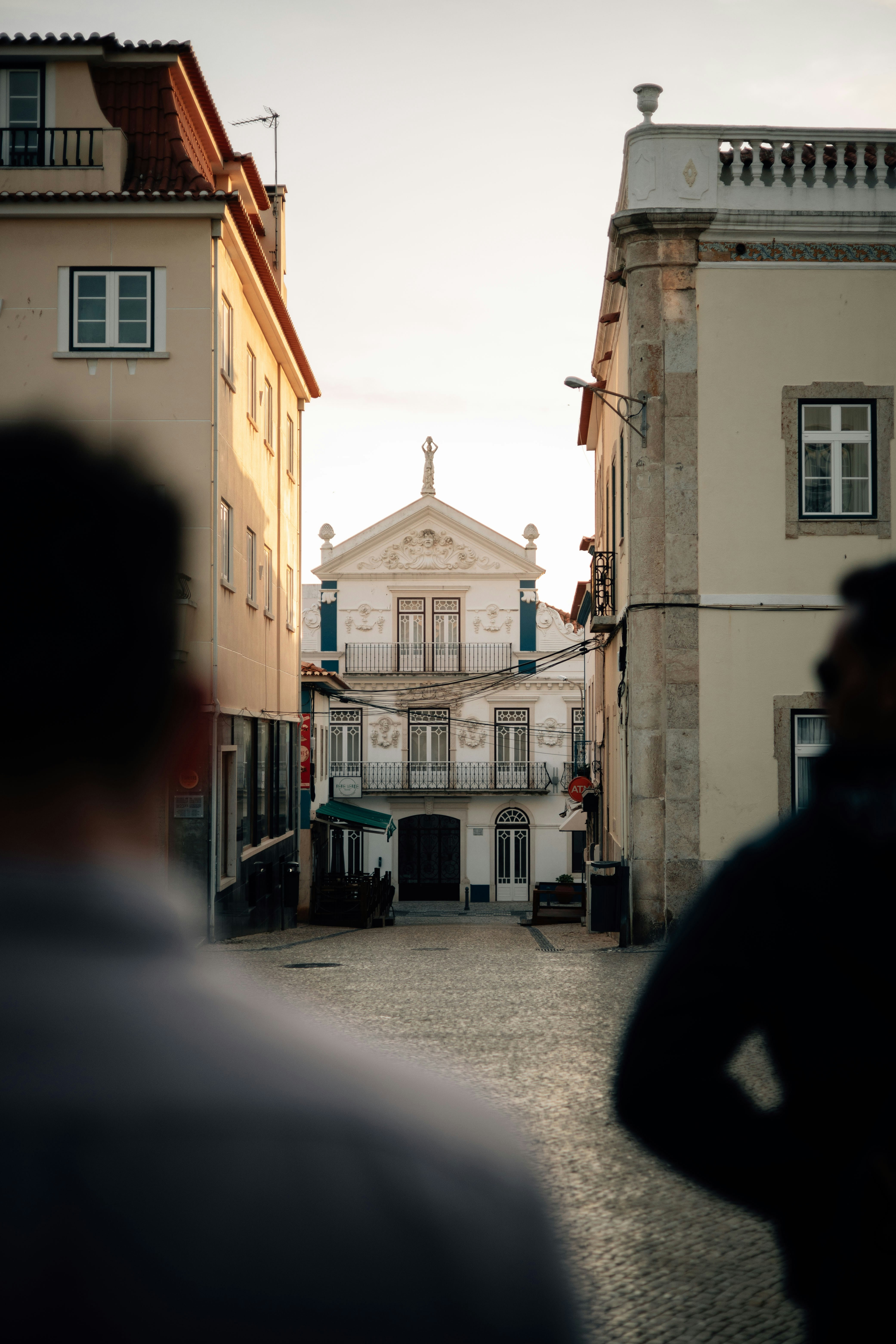 Historic building framed by modern structures in a cobblestone street, highlighting the blend of old and new architecture.