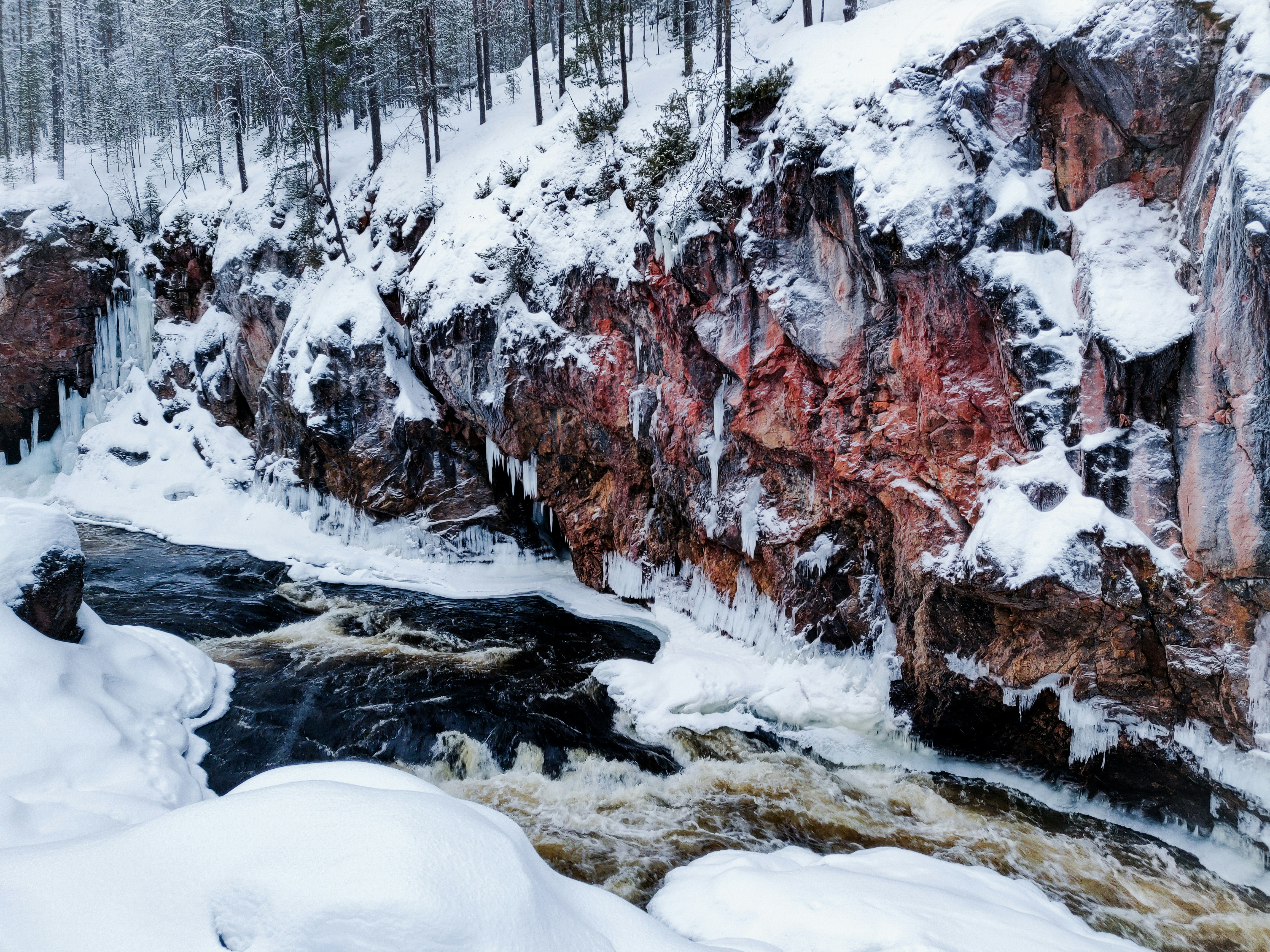 River cutting through snow-laden forest with striking red cliffs.