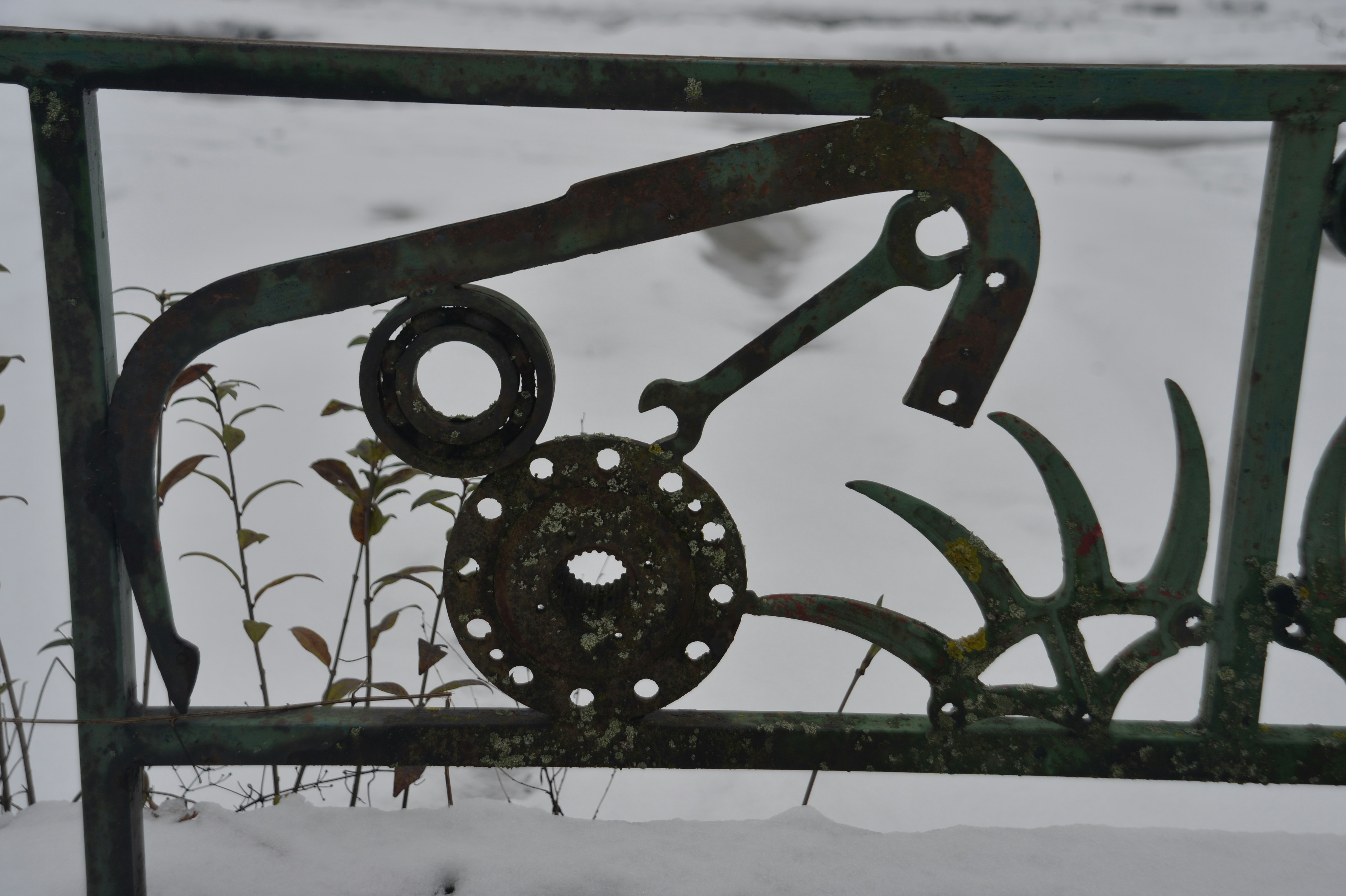 Snow-veiled gear motif on a rusted railing