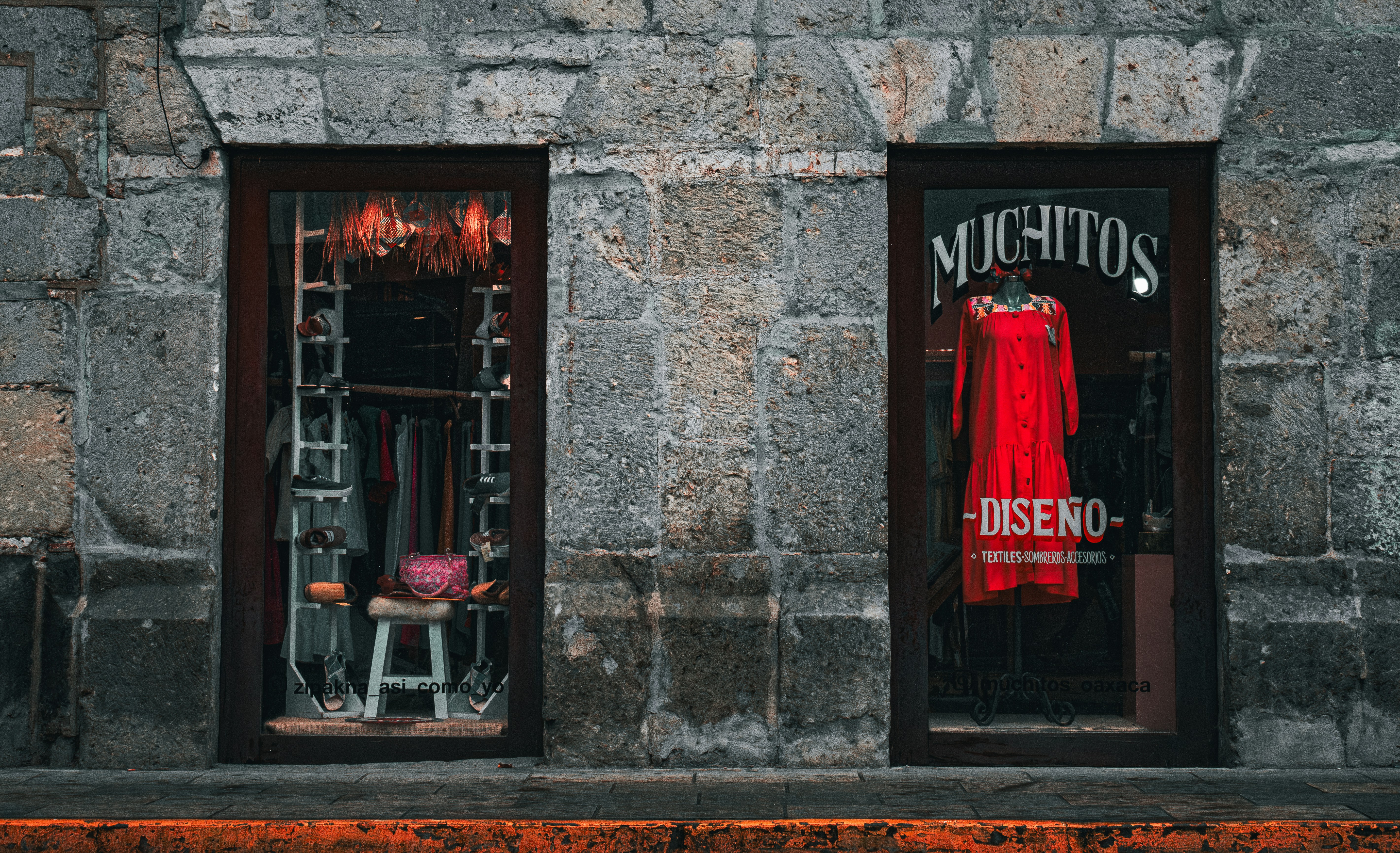 Stone façade with two window displays showcasing vibrant clothing against a rustic backdrop.