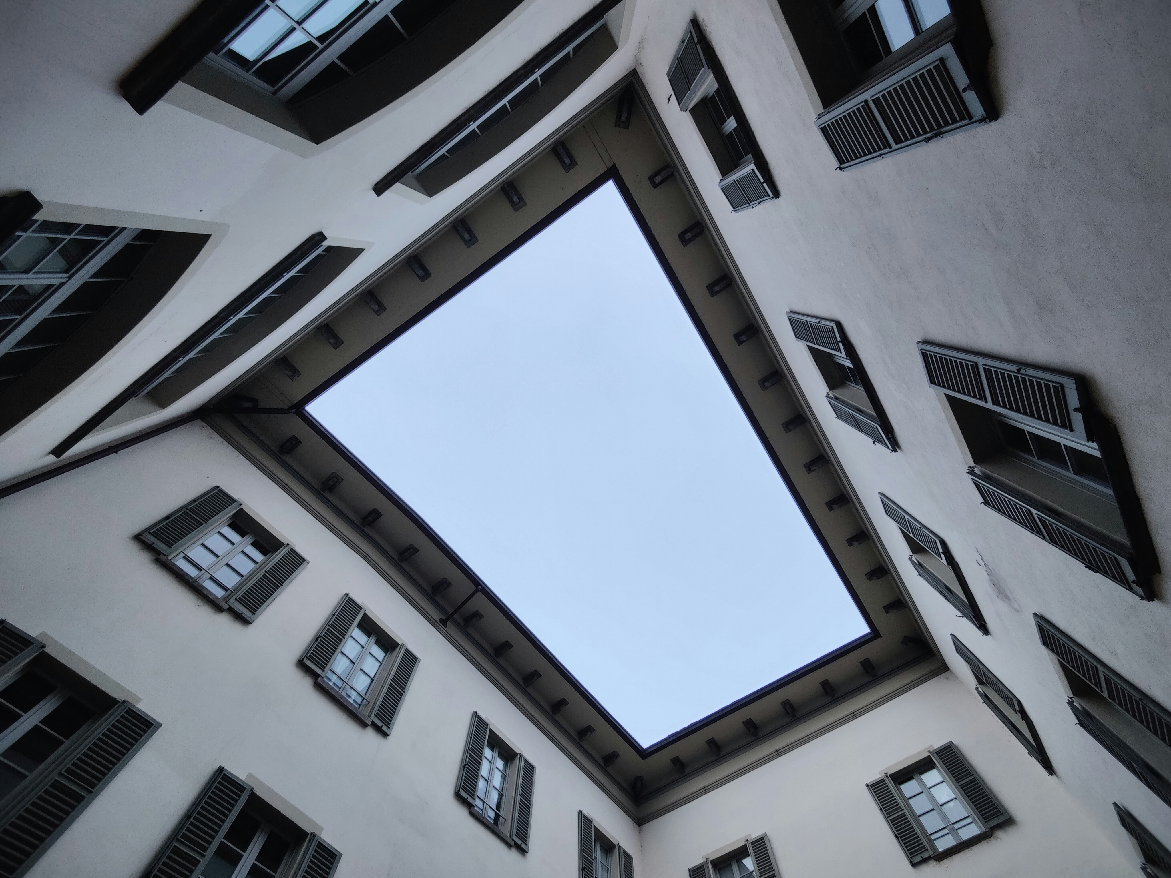 Open courtyard surrounded by tall buildings with an angular skylight view.