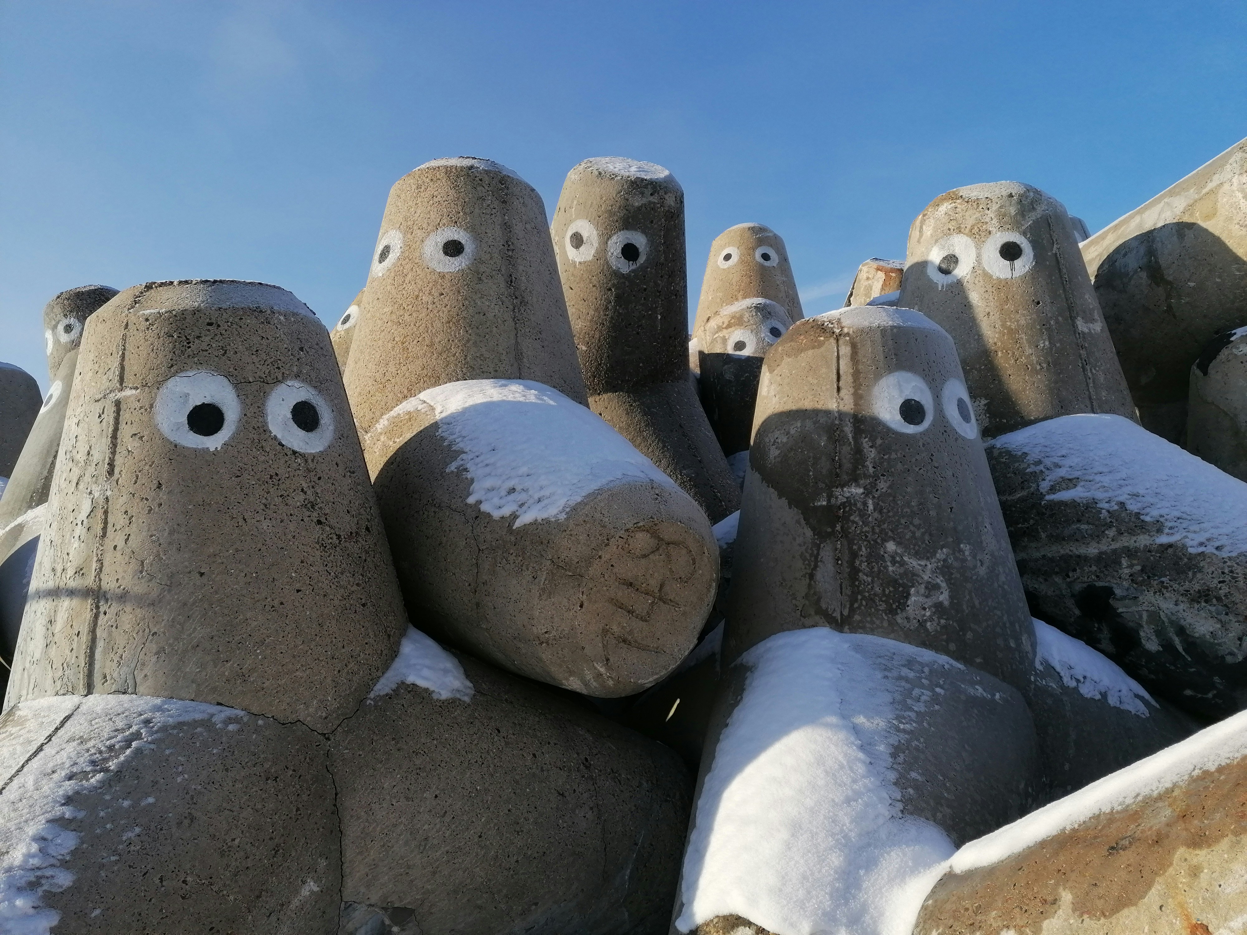 Row of concrete tetrapods along a breakwater wear playful white-eye faces, turning a coastal barrier into a whimsical lineup.