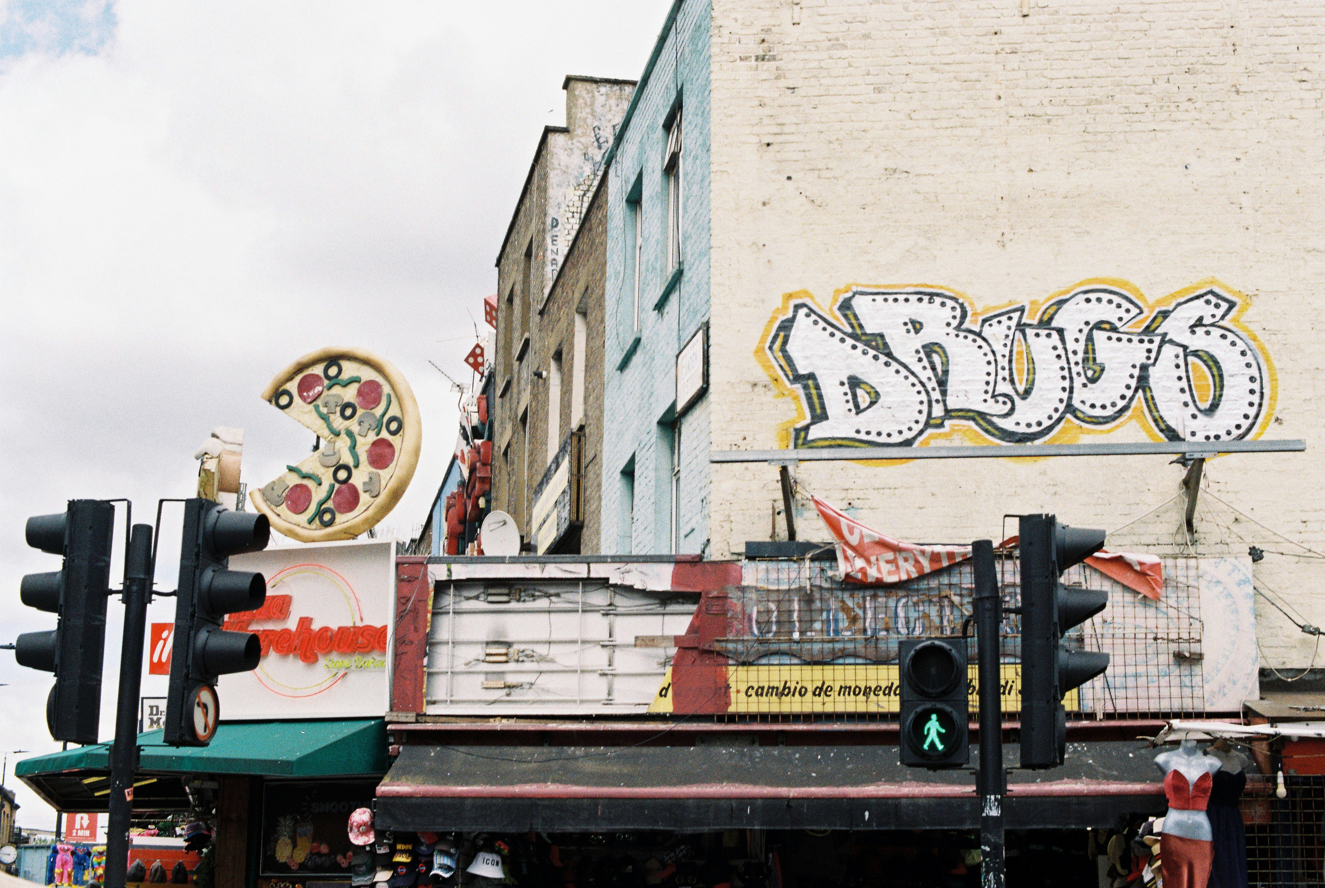 Graffiti-covered building with a large pizza sign and traffic lights in the foreground.