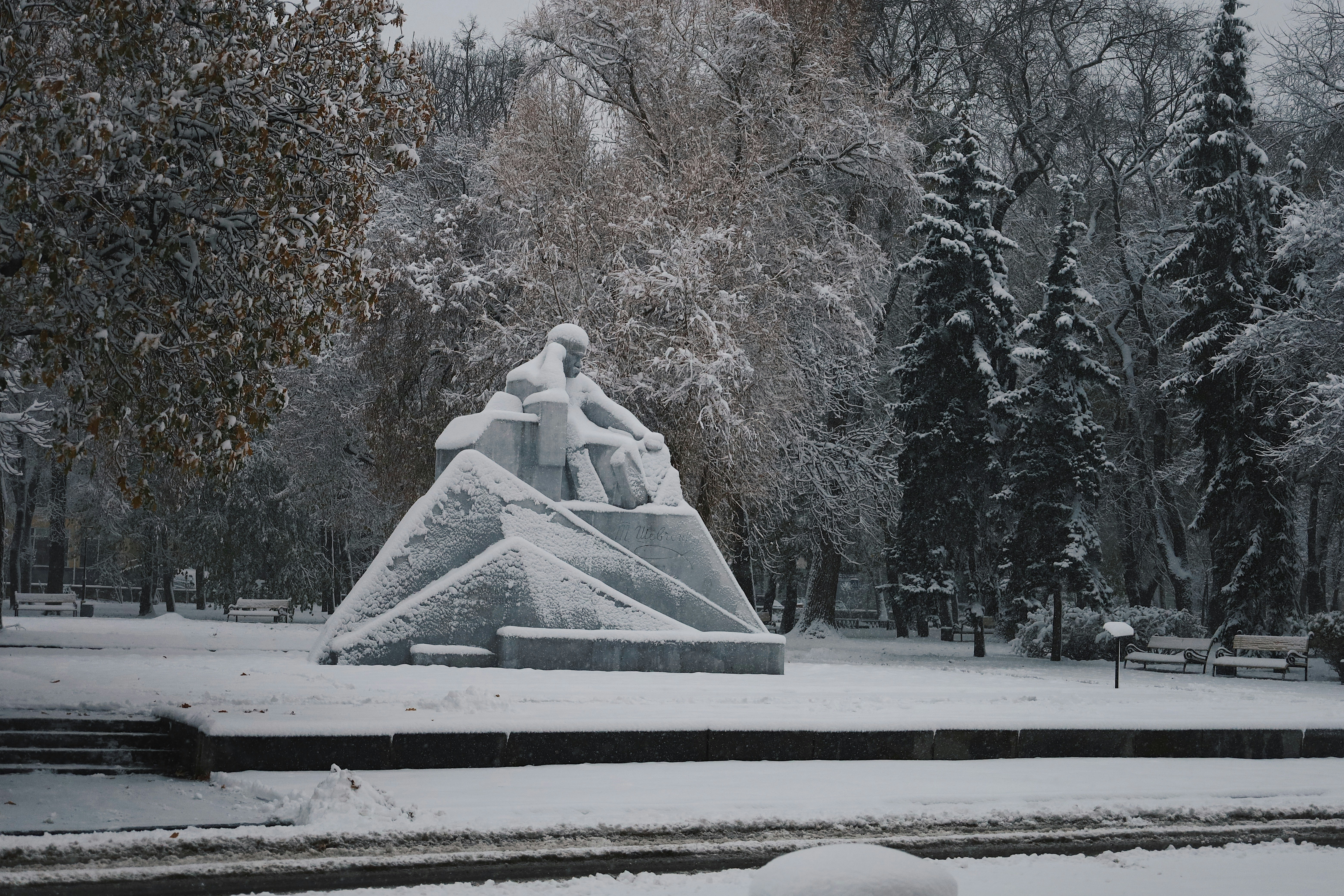 a snow covered park with a statue in the middle of it