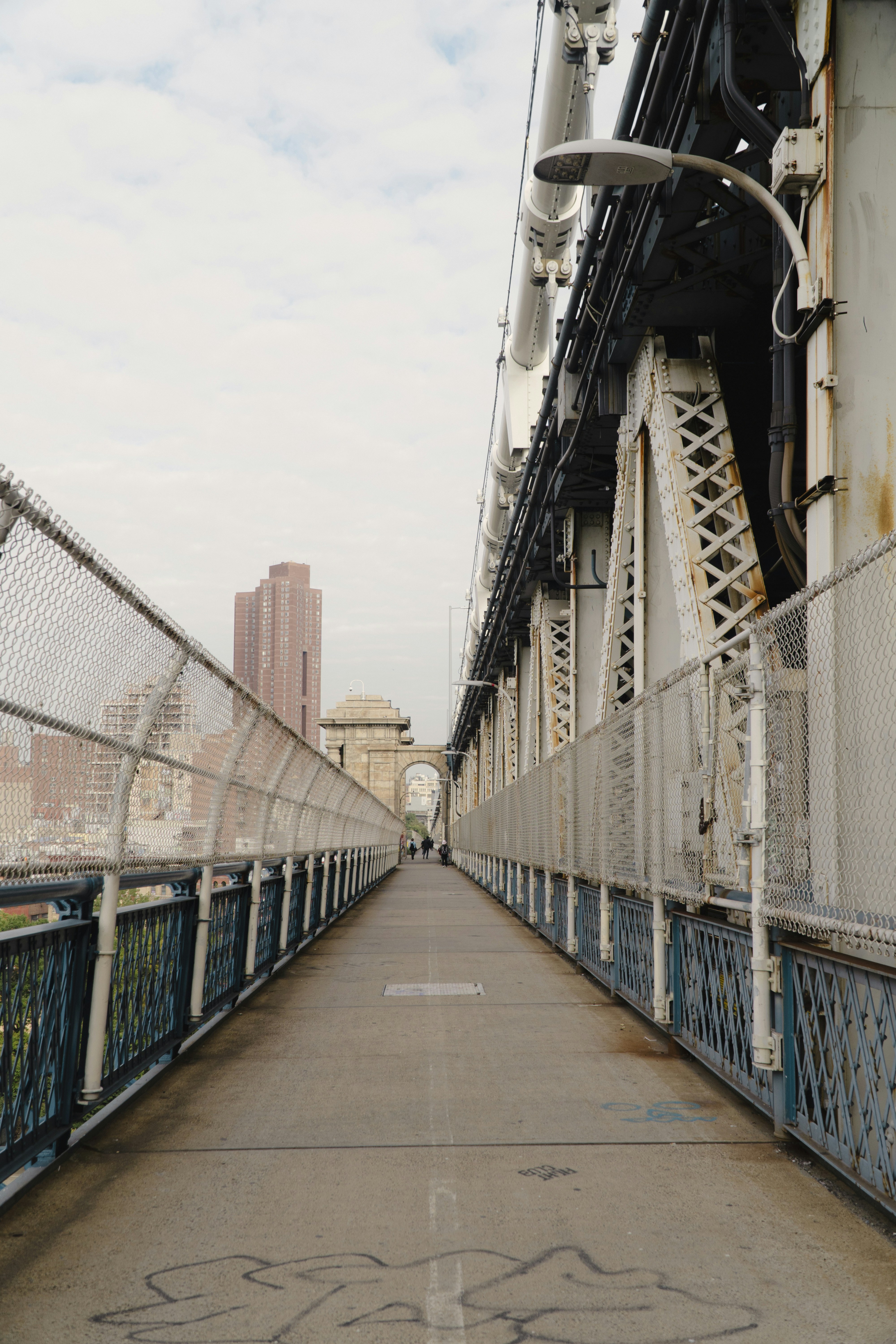 Pedestrian walkway on a bridge flanked by industrial elements and city skyline in the background.