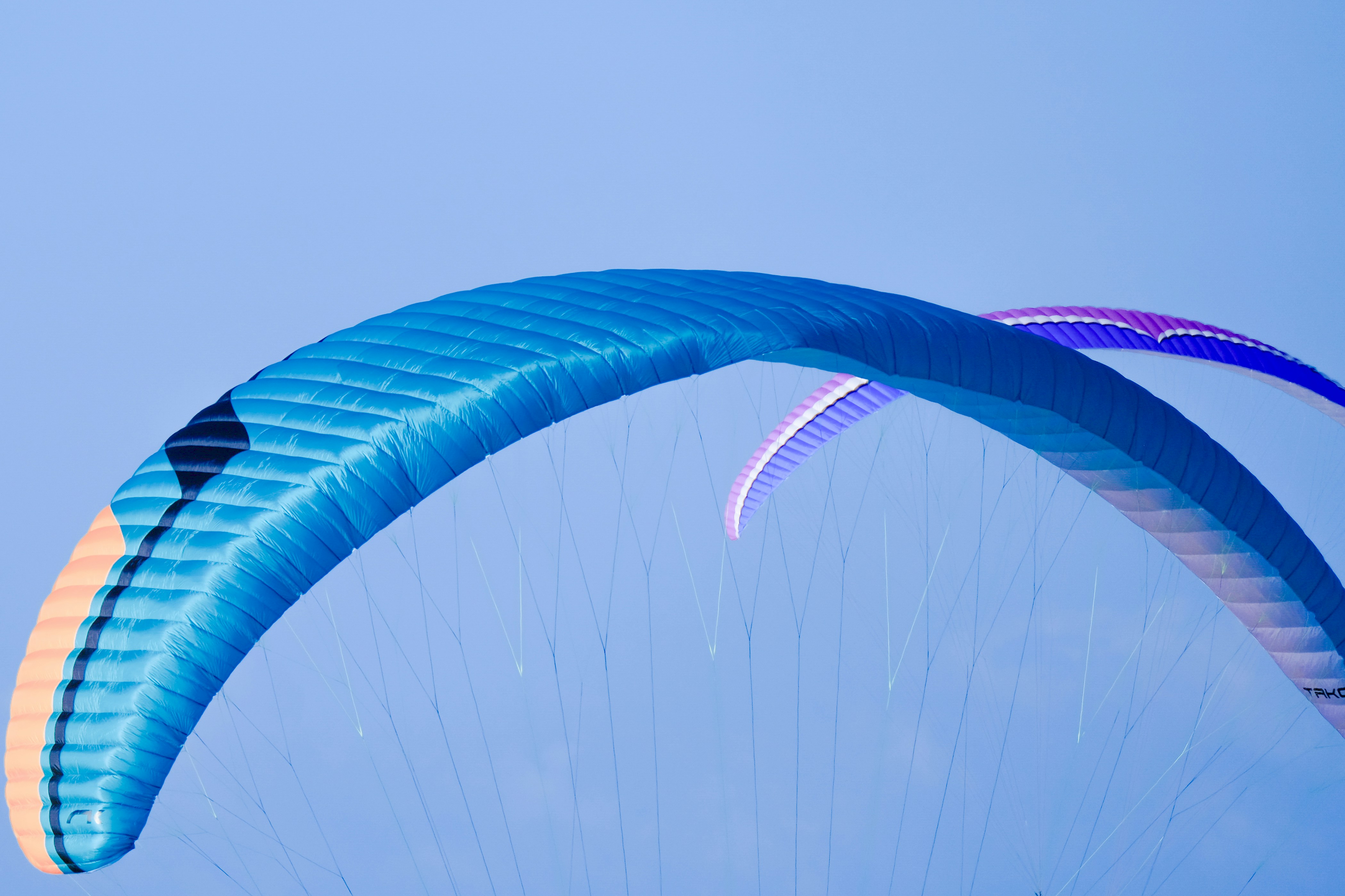 Blue Arc in a Clear Sky: Paraglider Wings in Flight