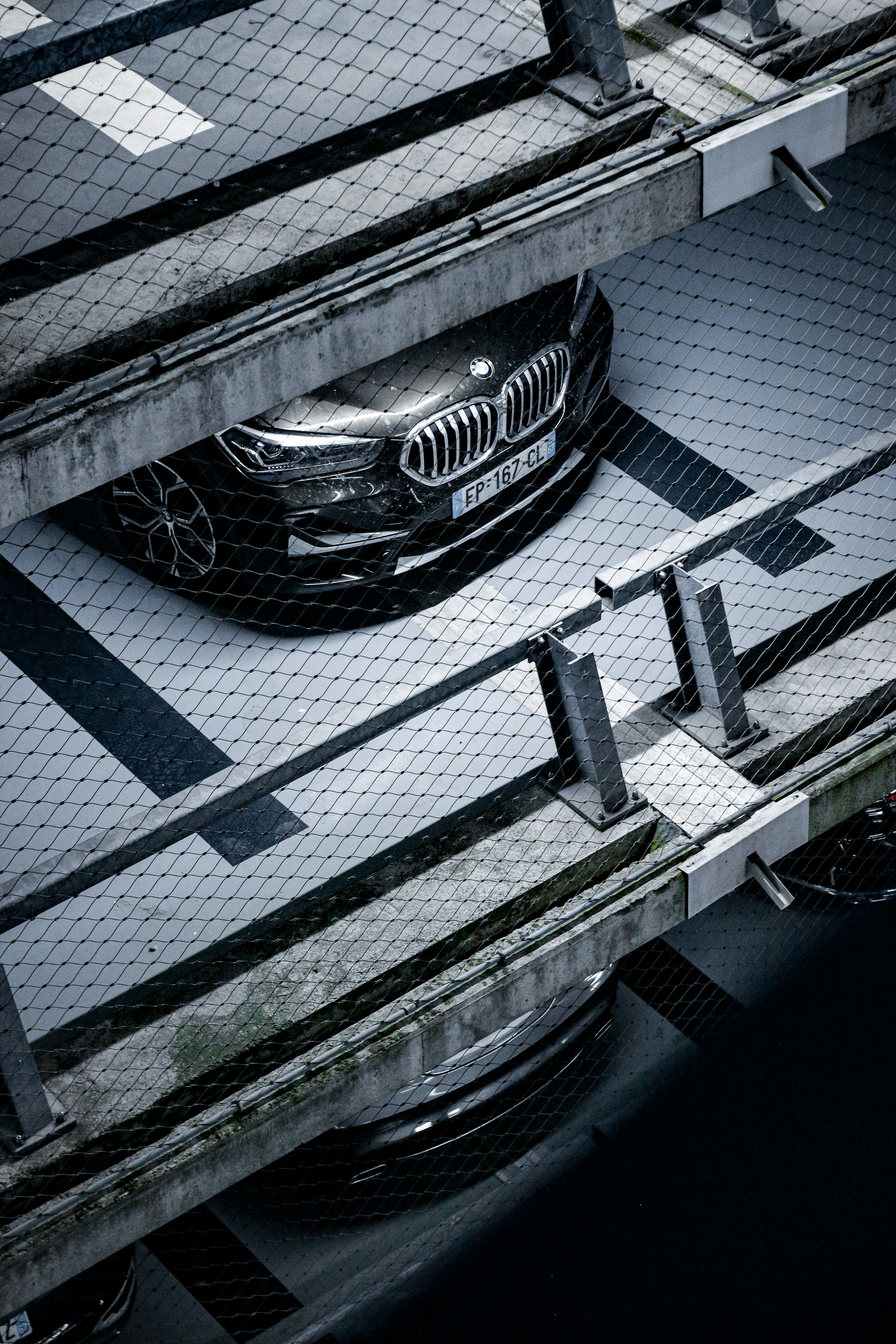 Geometric Confinement: BMW Front Grille Through Chain-Link on a Concrete Parking Deck