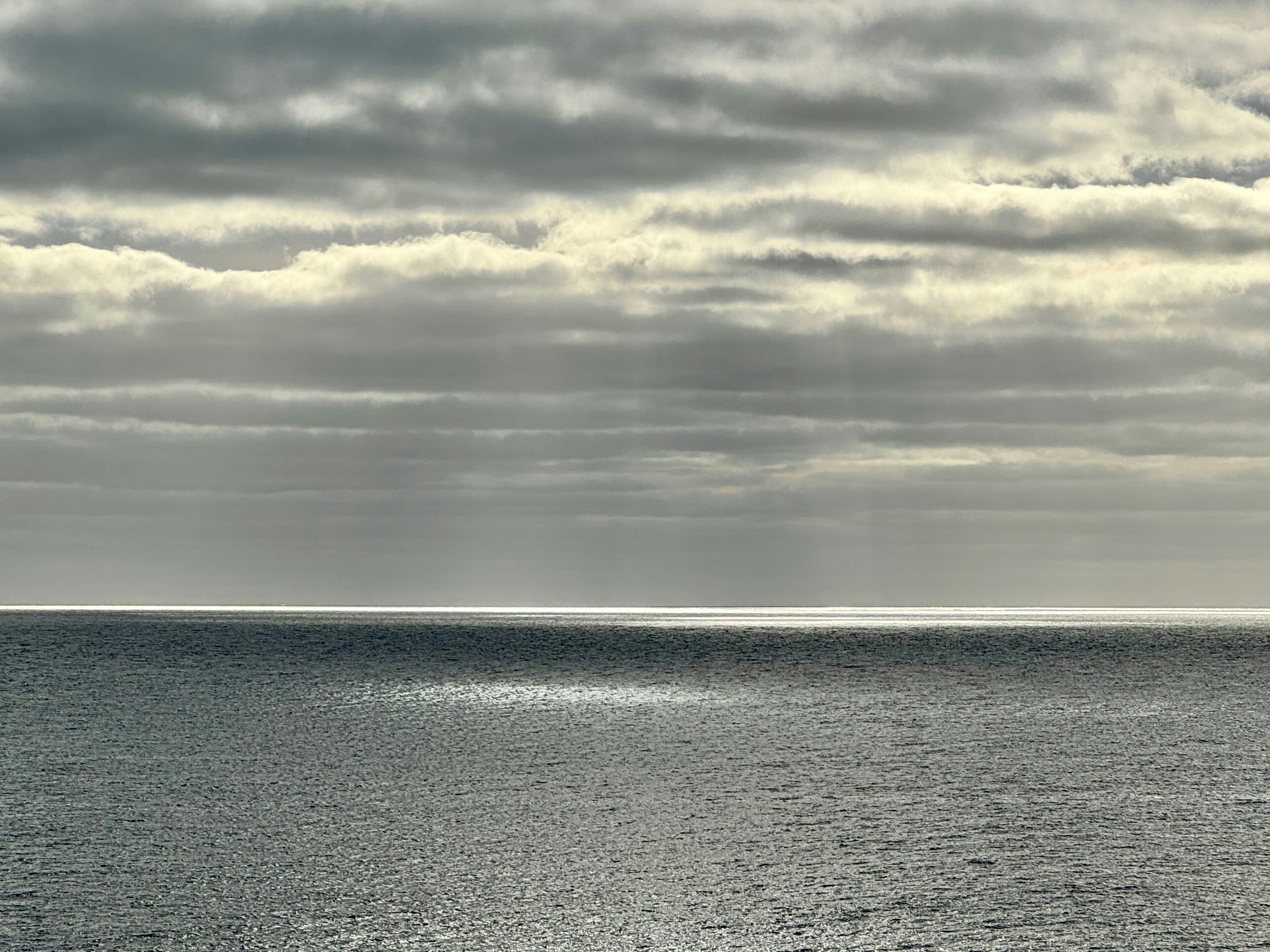 Calm sea under a cloud-speckled sky with soft morning light illuminating the horizon.