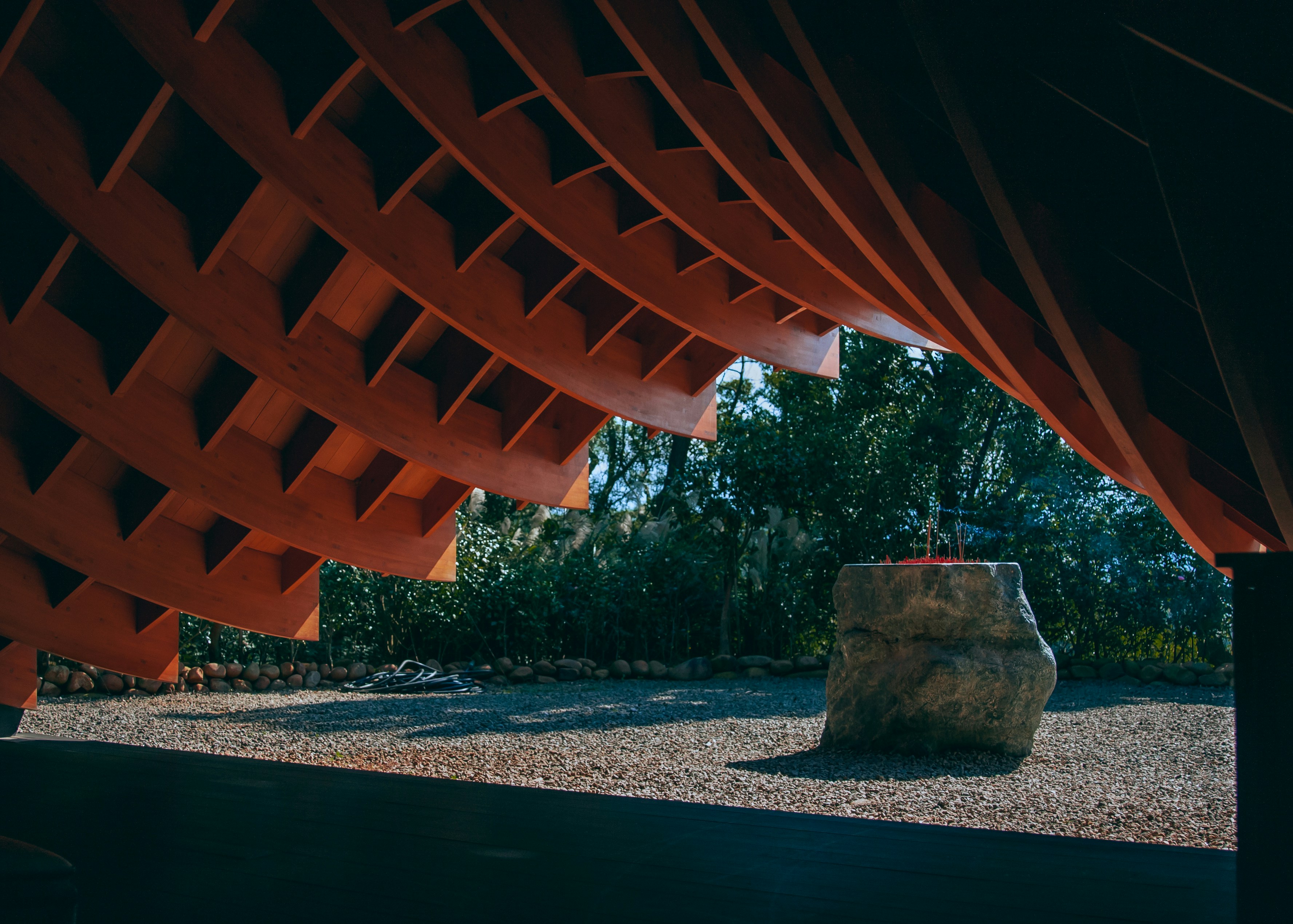Modern architectural structure with red geometric patterns framing a sunlit garden.