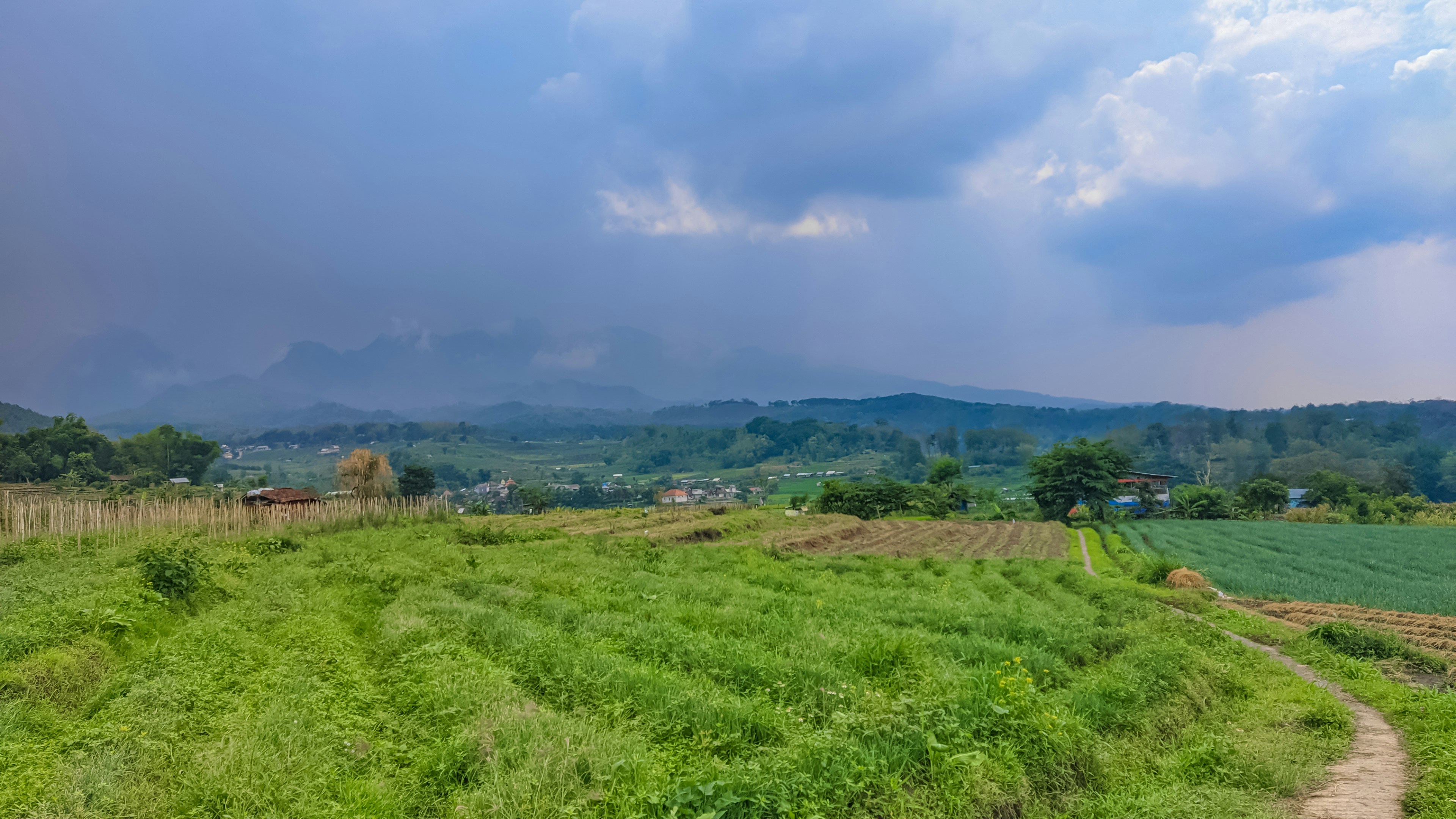 Lush green fields stretch towards distant hills under a dramatic, cloud-filled sky.