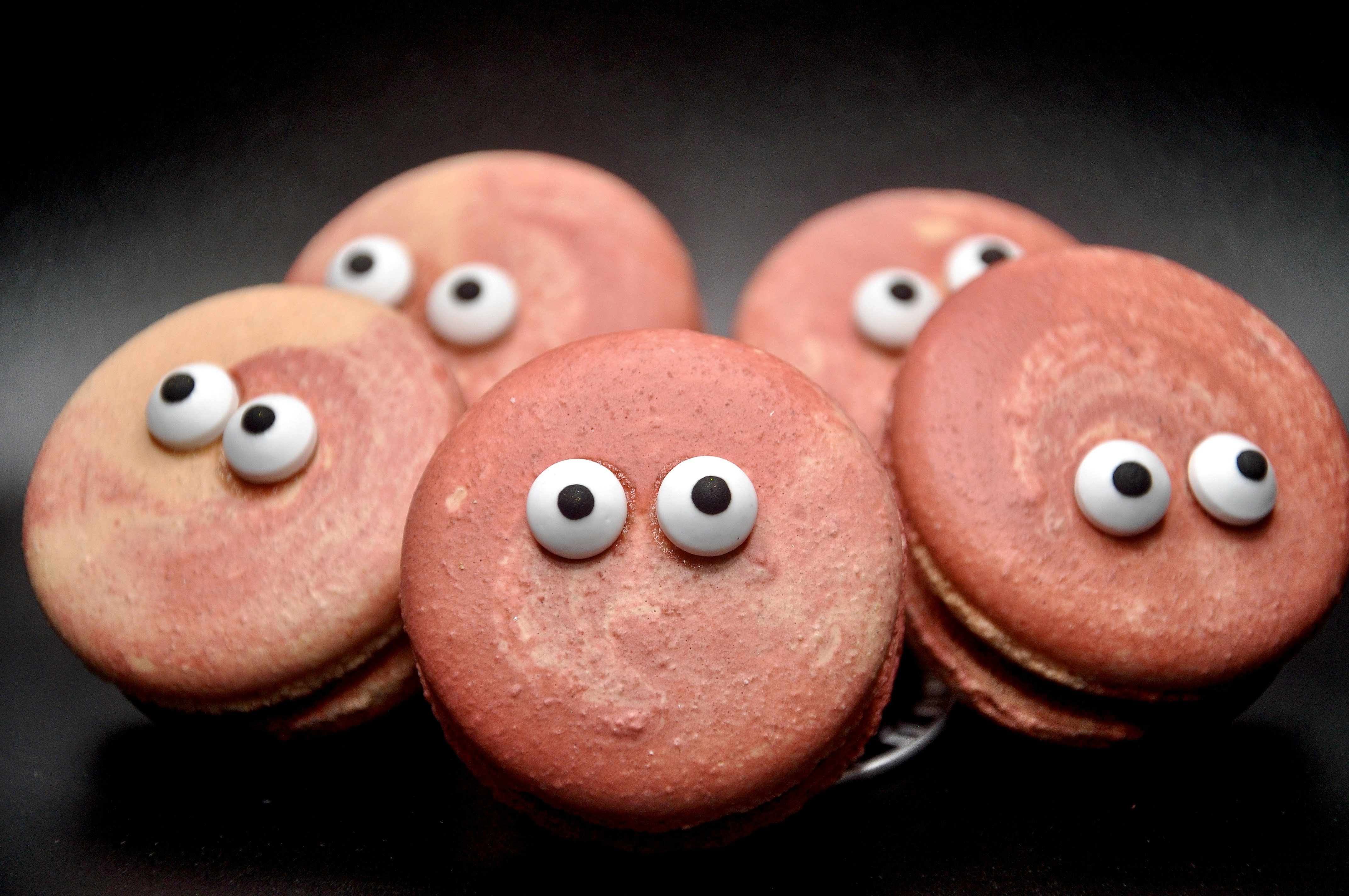 Group of Cheery Pink Macarons with googly eyes resting on a glossy dark surface