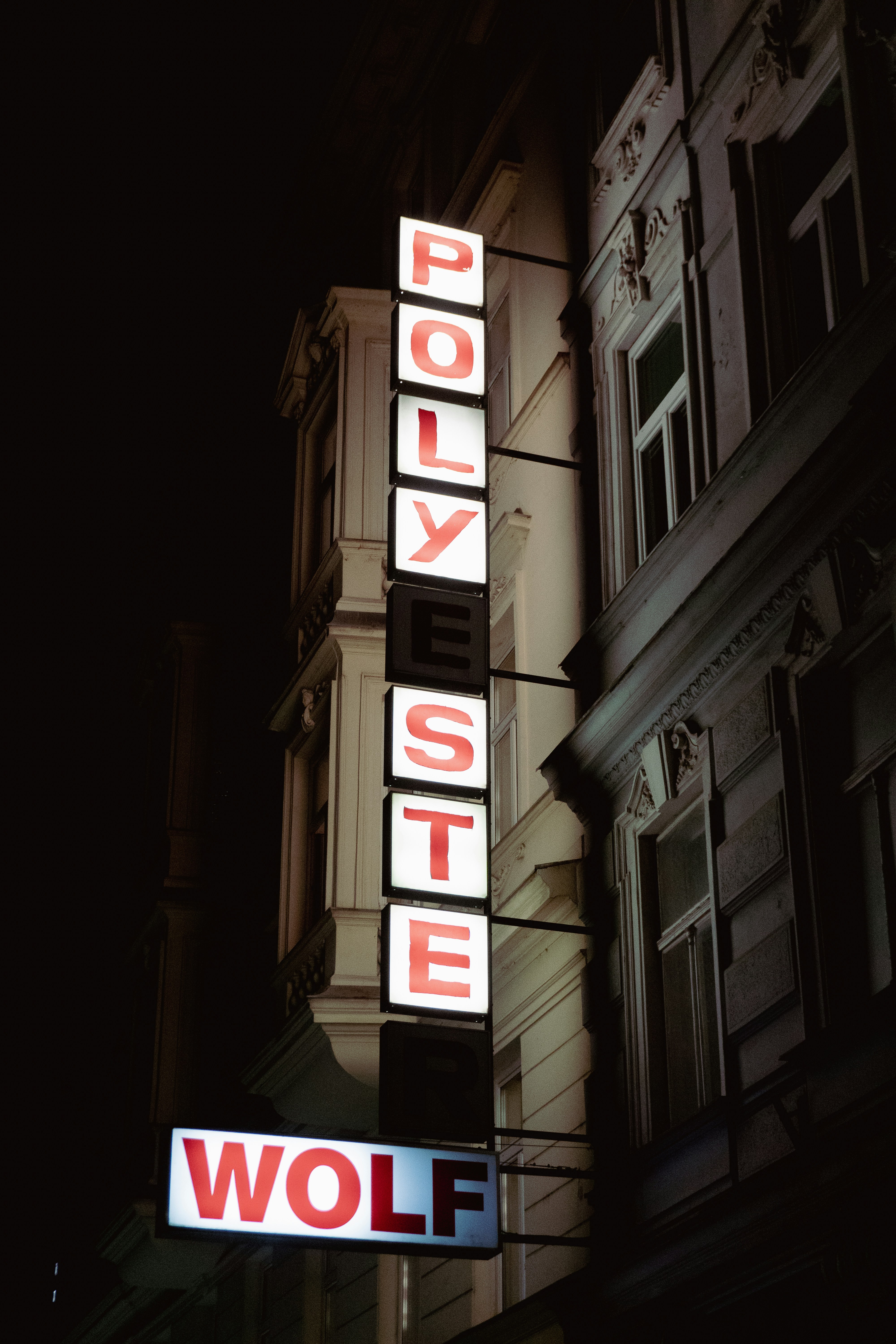 A vertical neon sign on a historic building, with POLY letters stacked above a blue WOLF panel, lit against the night.