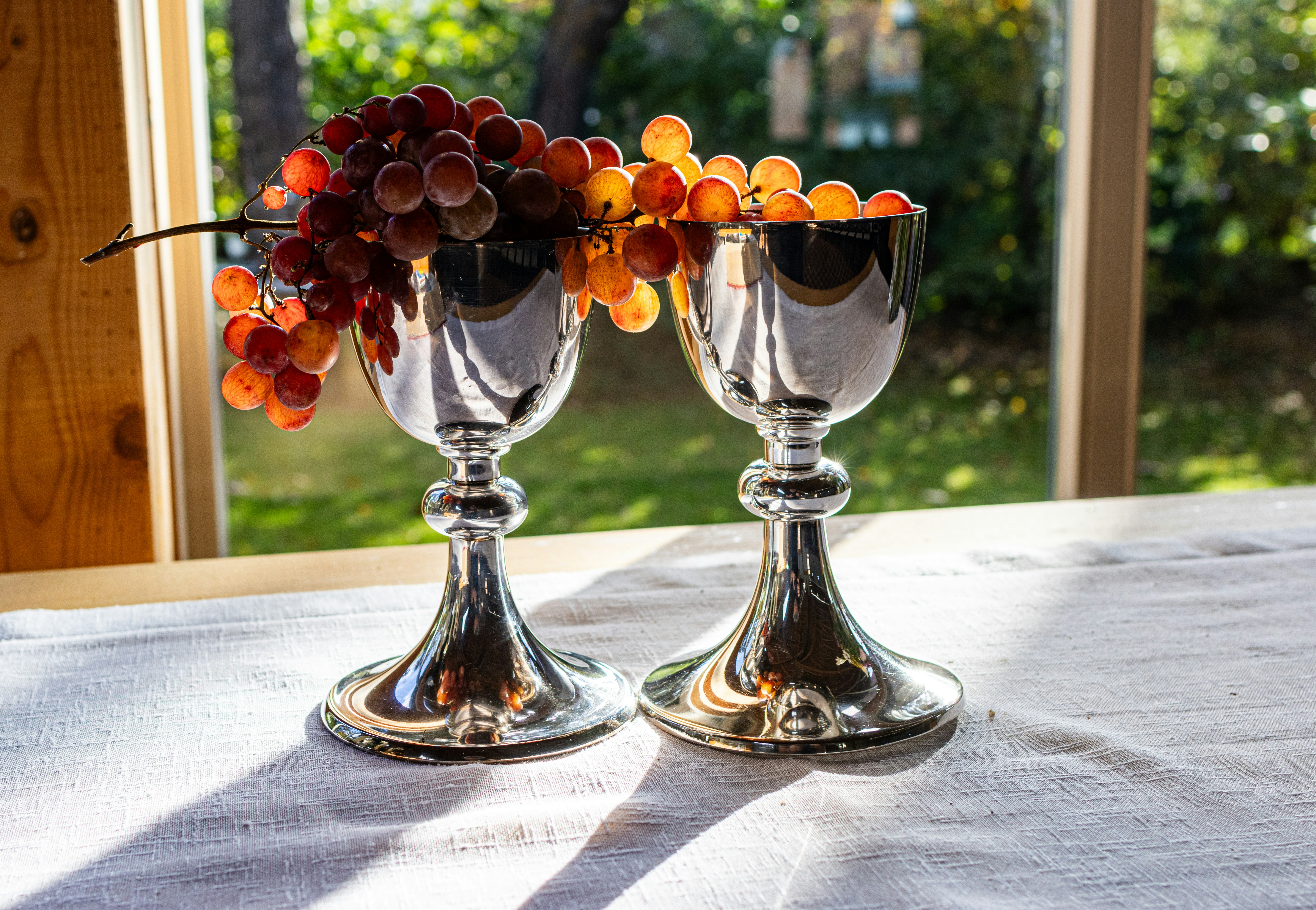 Sunlit Grapes Crowned by Silver Goblets: A Quiet Window Still Life