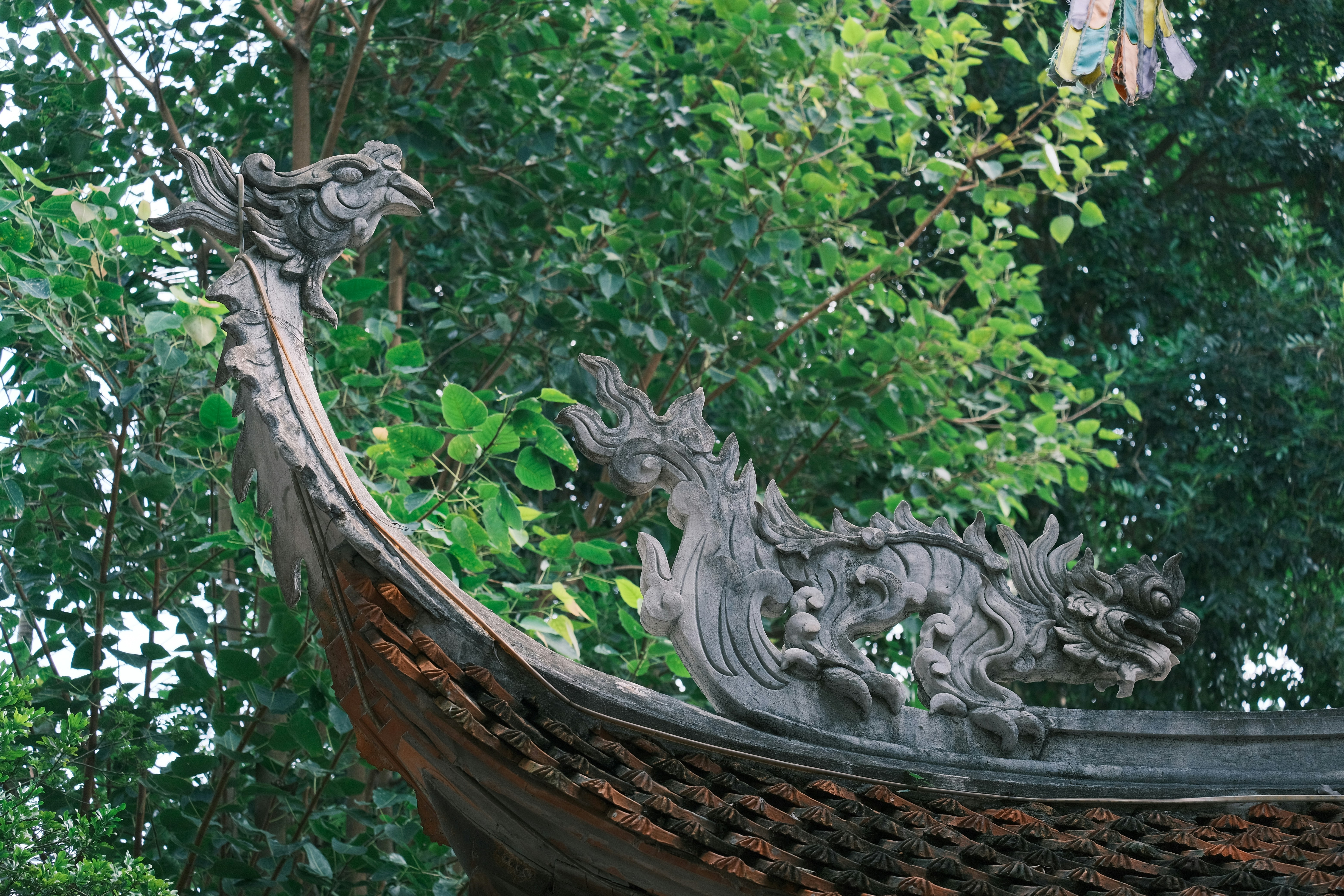 Intricate dragon motifs adorning the edge of a traditional roof, surrounded by lush greenery, showcasing cultural craftsmanship.