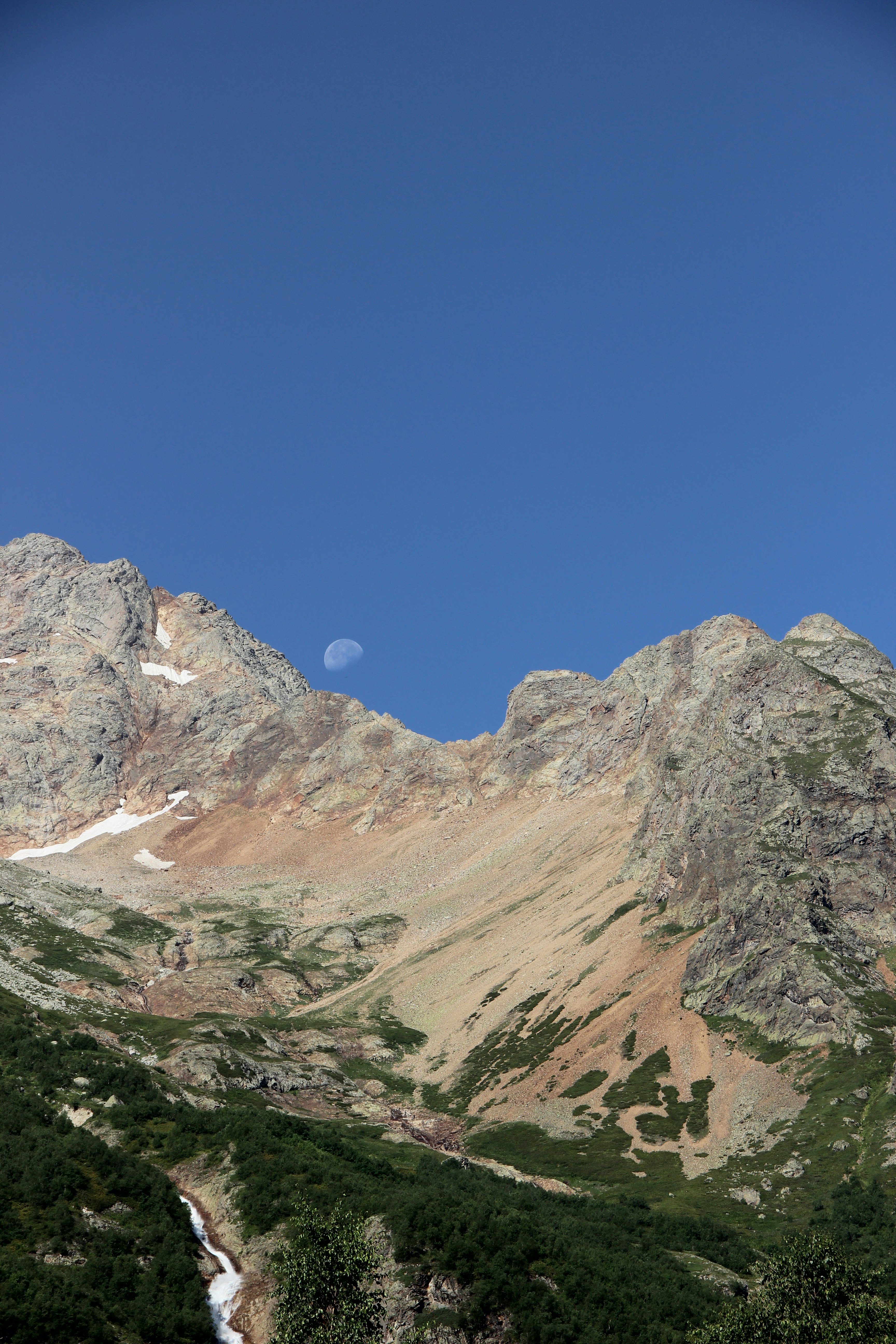 Moon Over the Crag: Alpine Ridge Under a Clear Blue Sky