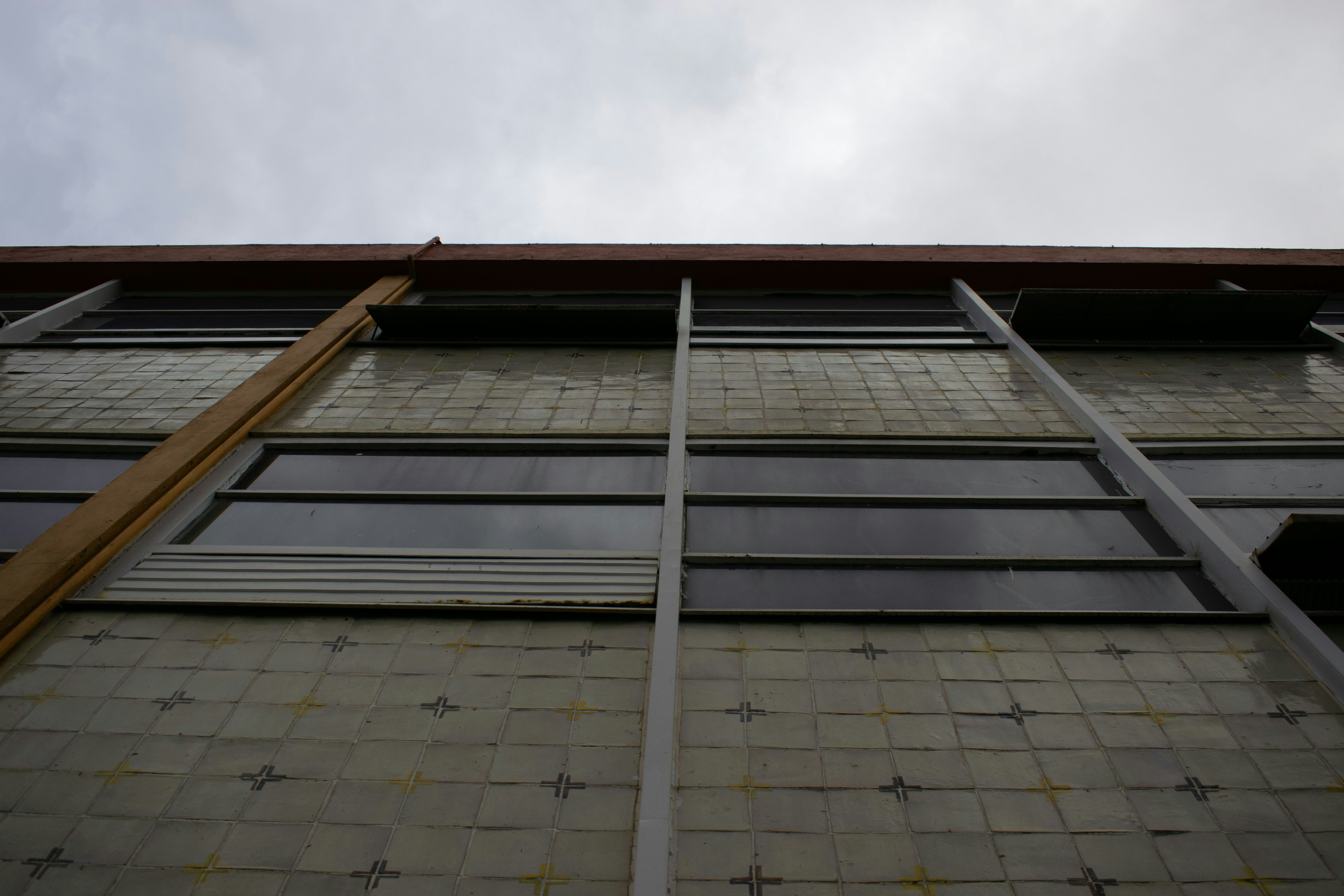 Upward view of a modern building facade with geometric lines and cloudy sky.