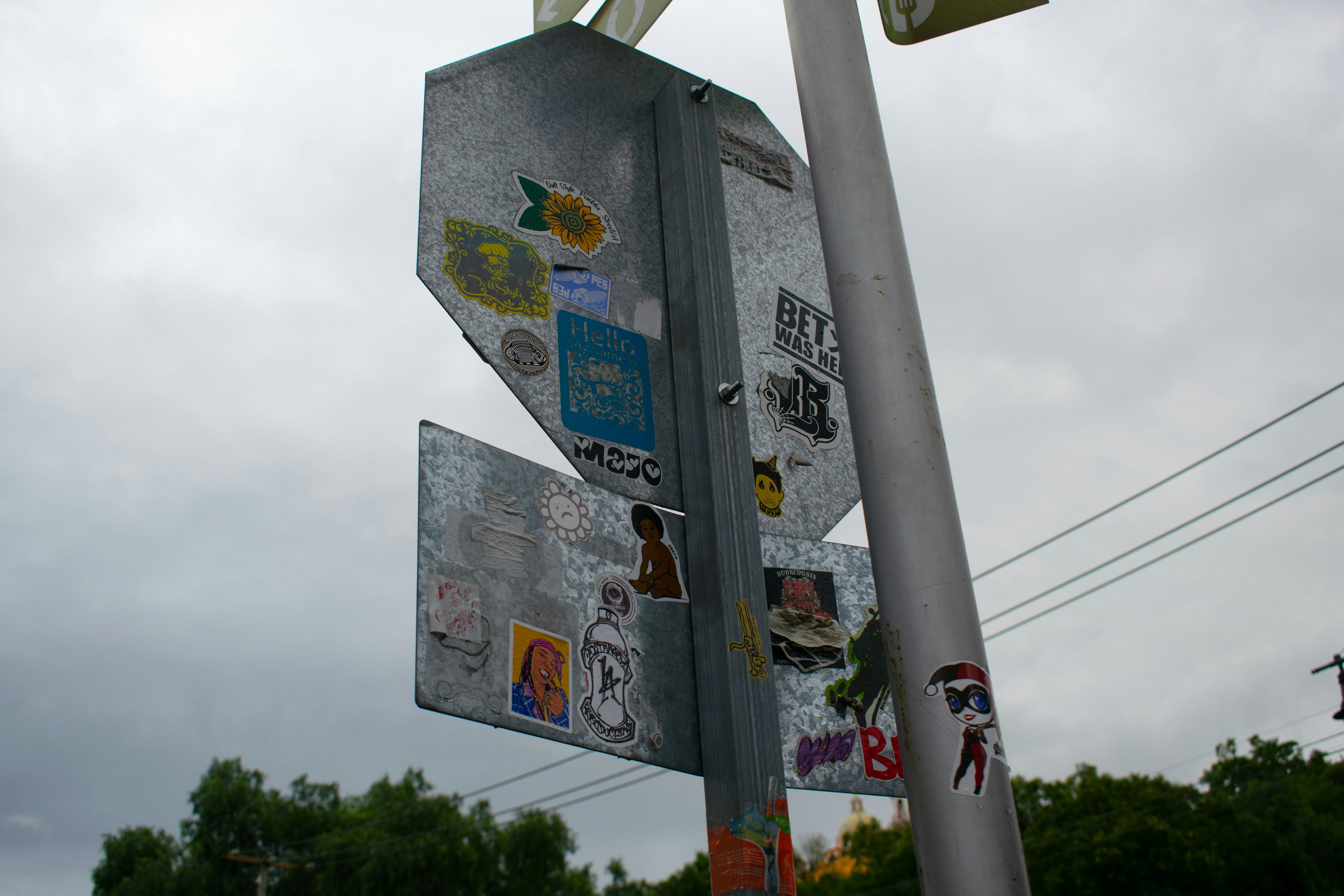 Stickered Sentinel: Patchwork Signpost Under an Overcast Sky