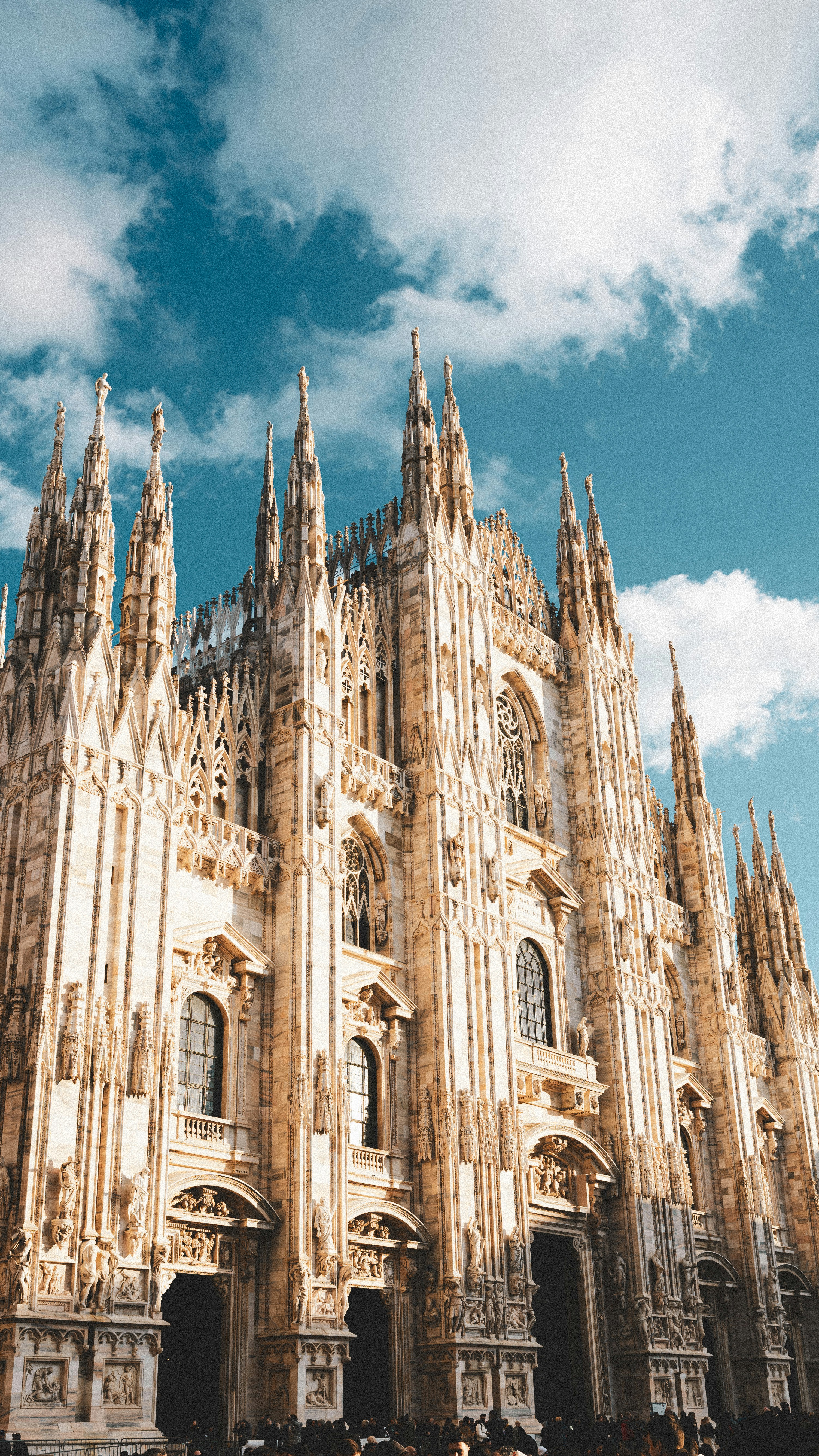 Intricate Gothic architecture of a cathedral against a vibrant sky, showcasing ornate spires and detailed sculptures. The scene captures the grandeur of historical craftsmanship.
