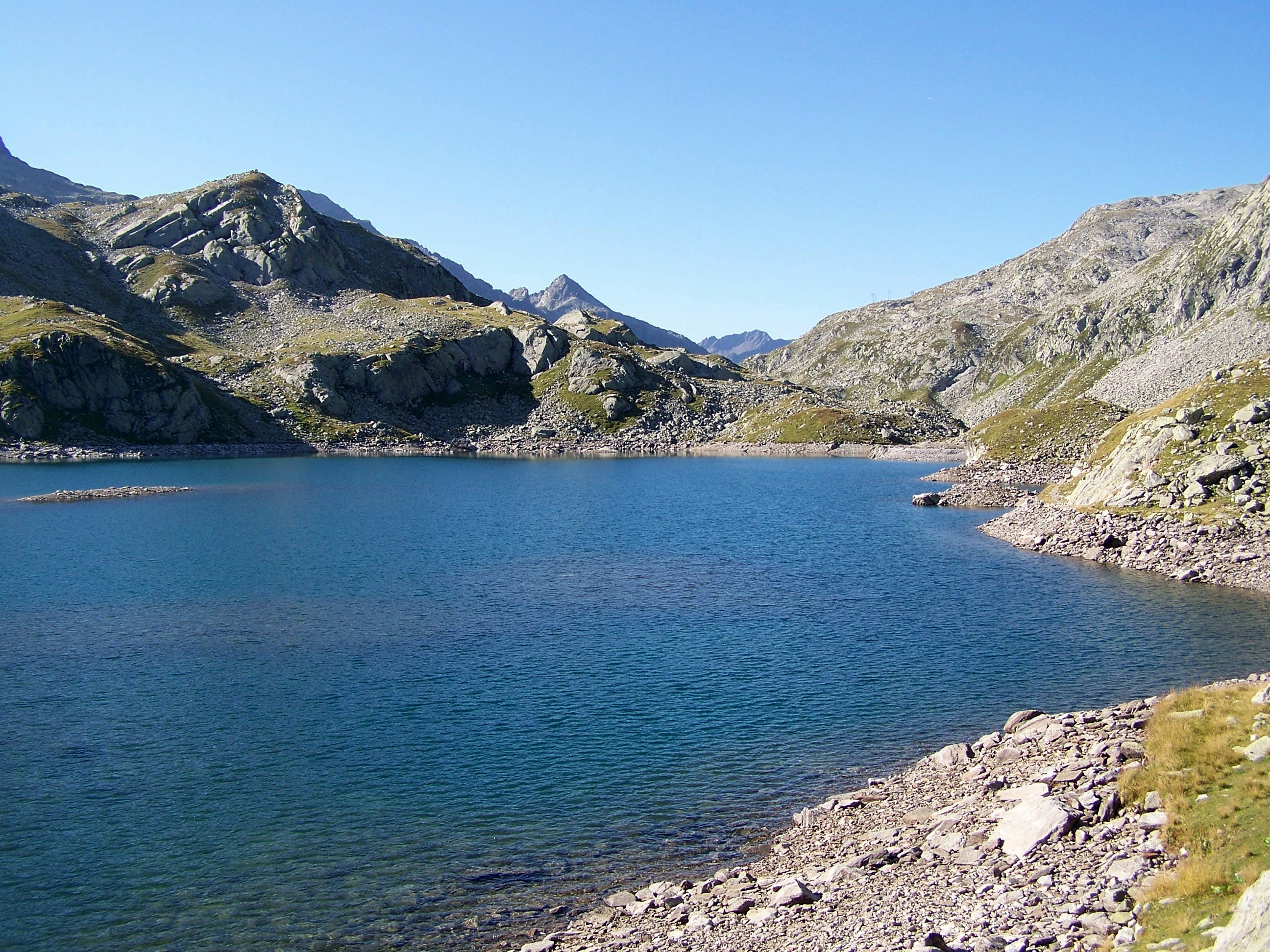 Tranquil alpine lake surrounded by rugged mountains under a clear blue sky.