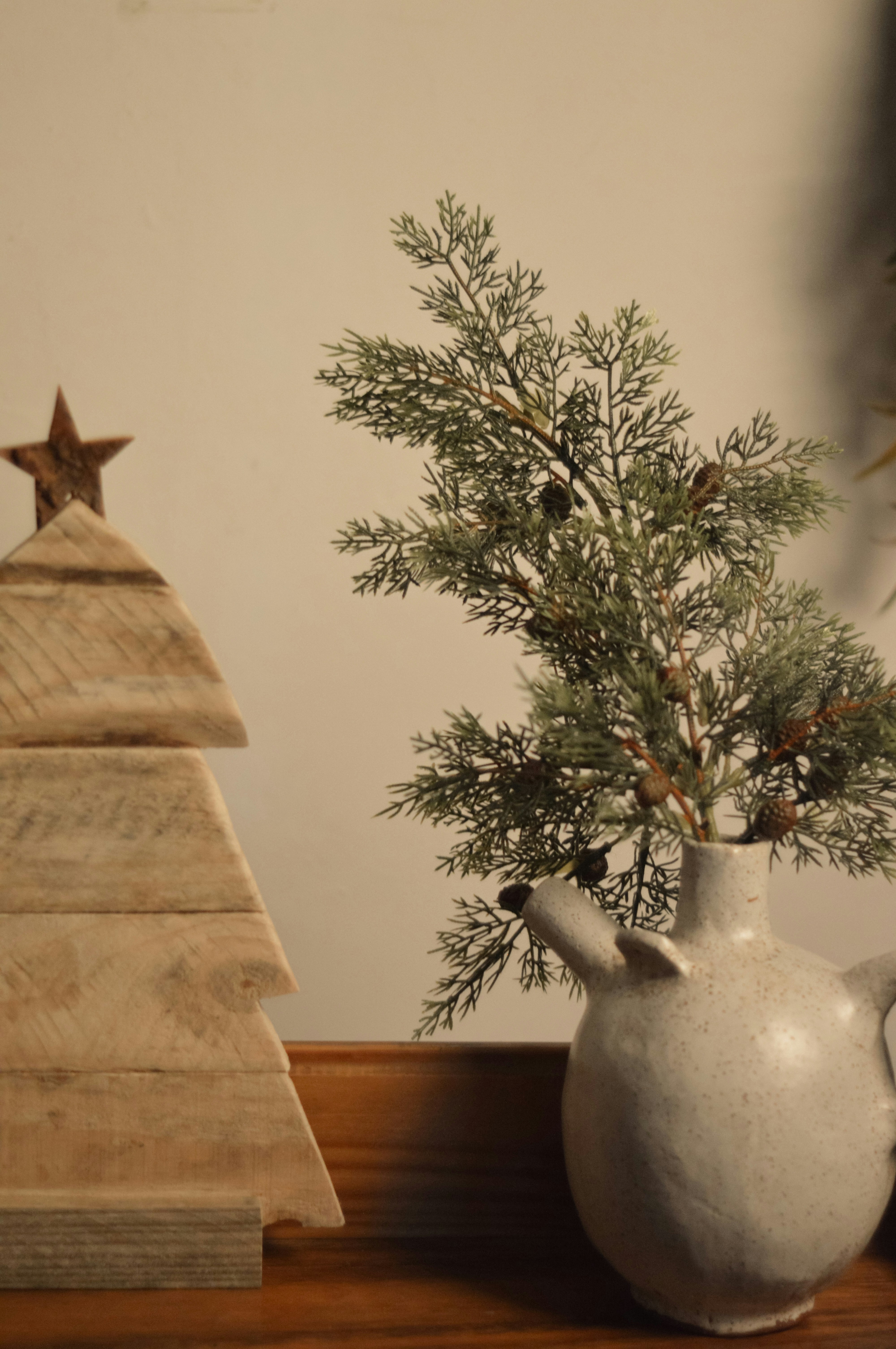 Minimalist vignette: pine stems in a ceramic vase beside a rustic wooden Christmas tree