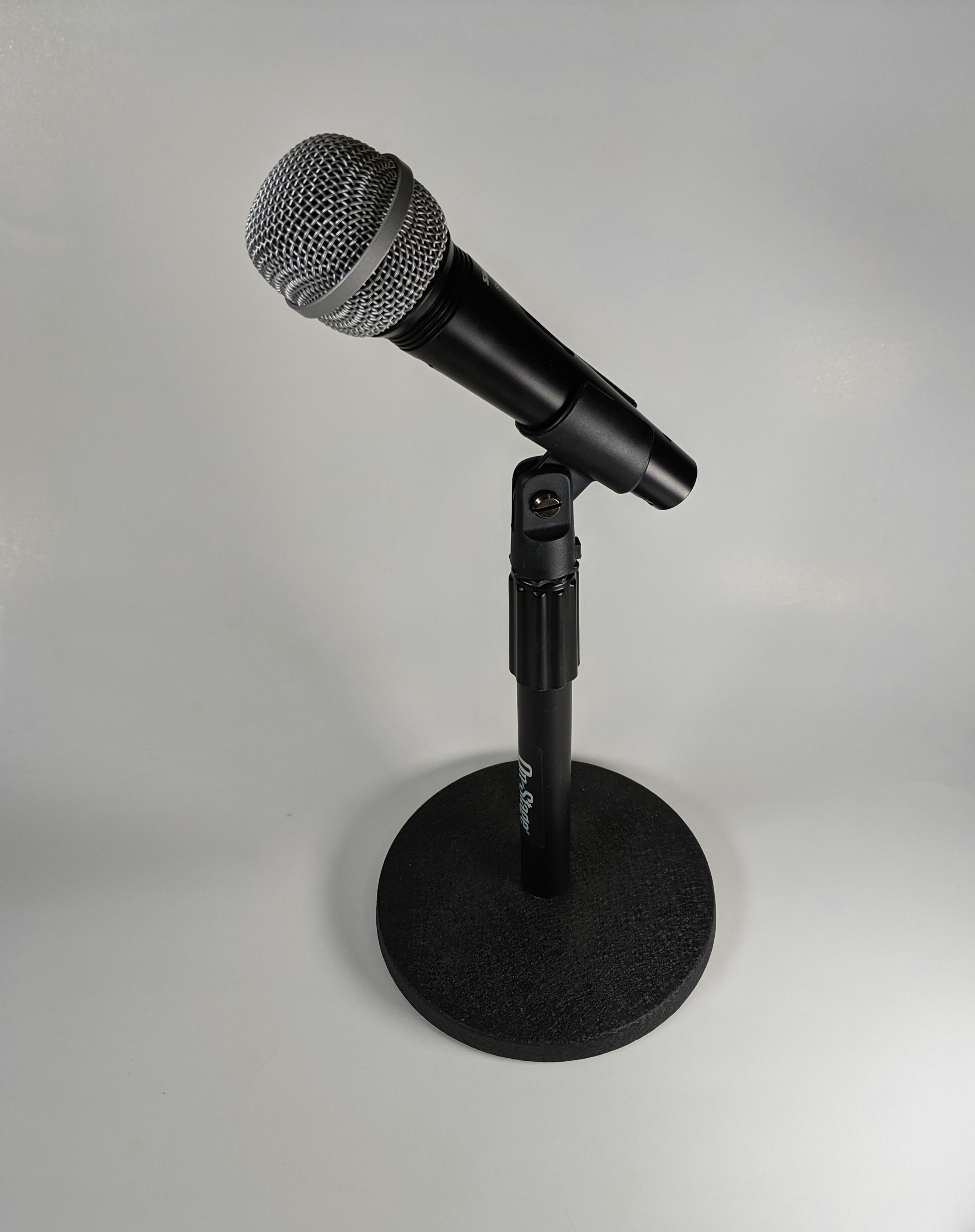 Black microphone on a sturdy stand against a neutral background, emphasizing its role in performance and communication.