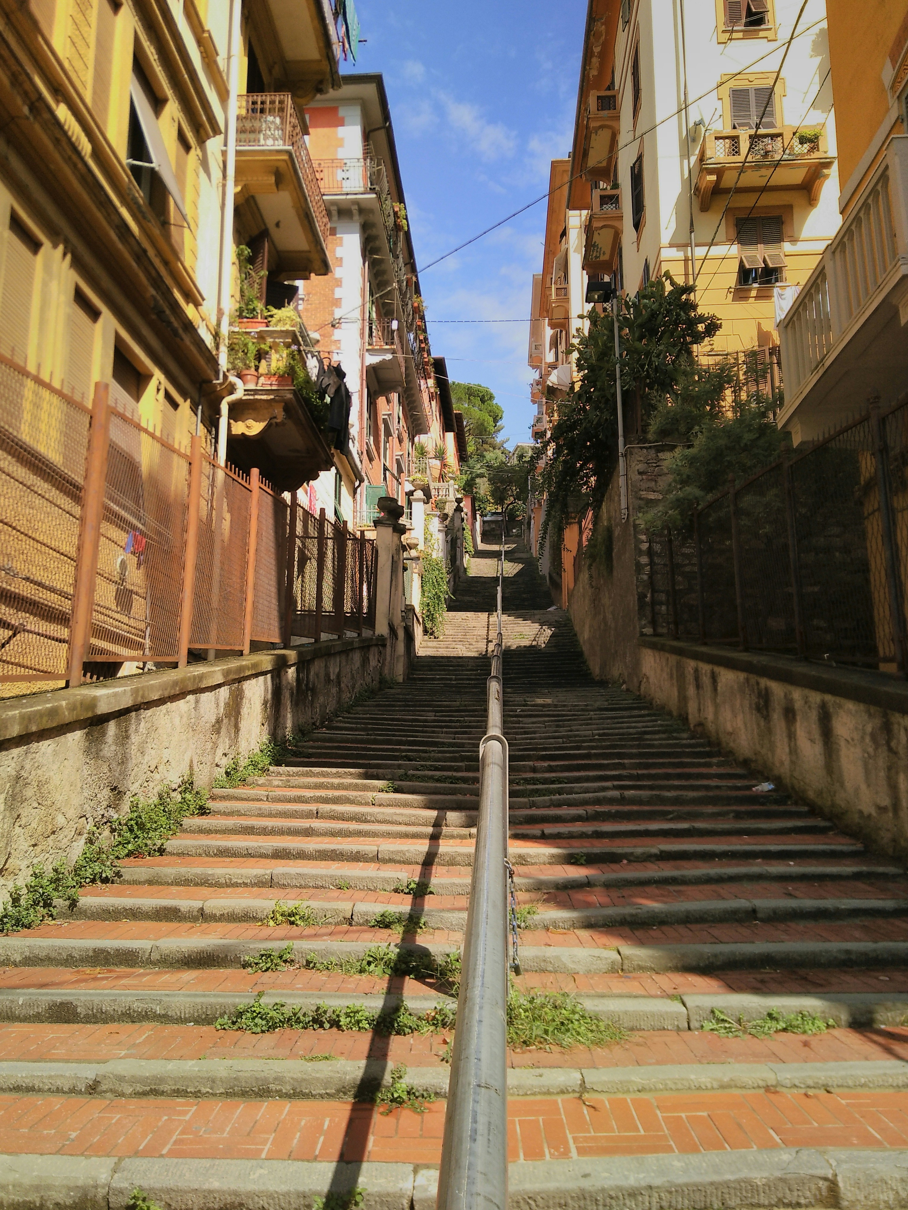 Centerline Ascent: Sunlit stairs between warm apartments toward a clear city sky