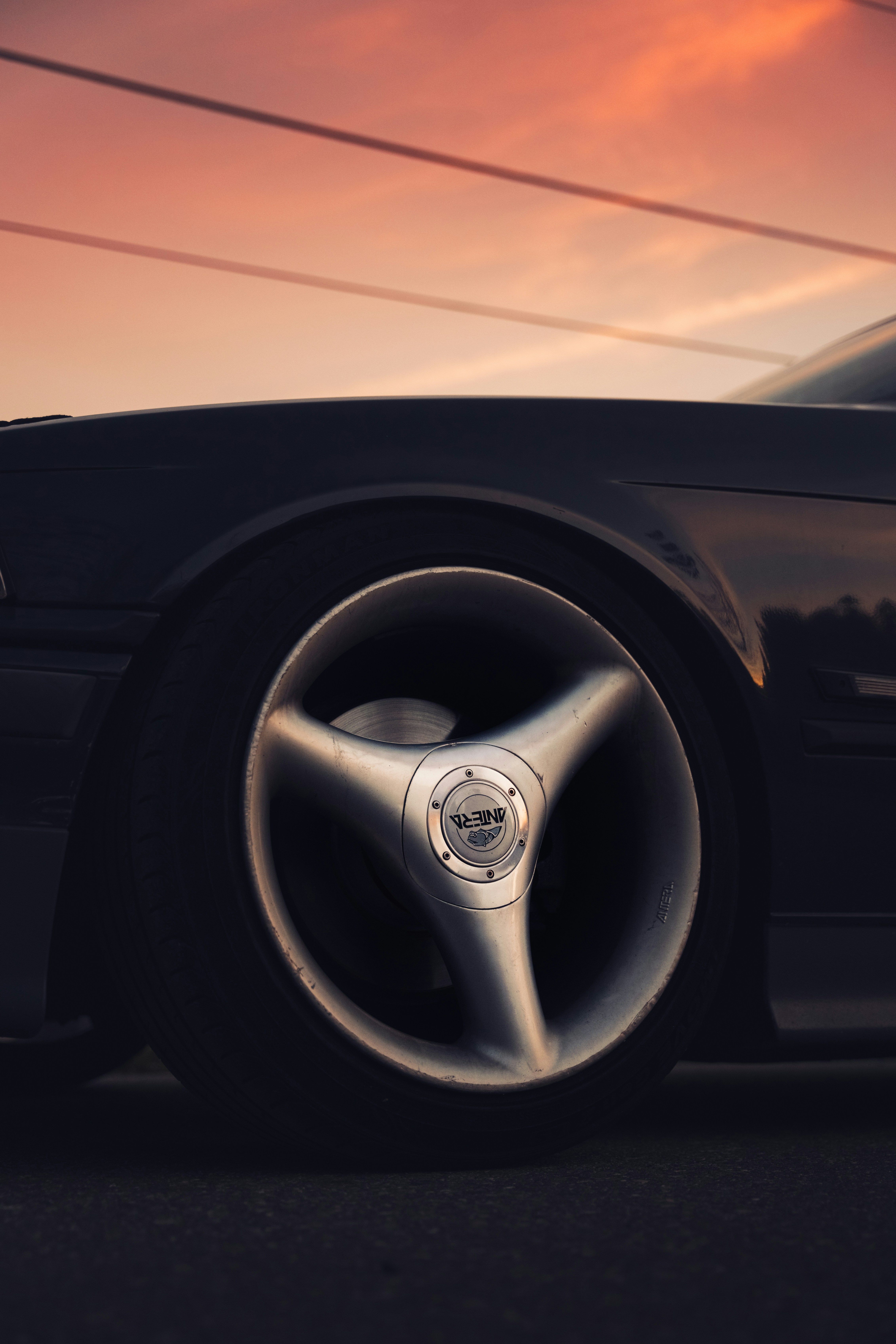 Sunset Over a Three-Spoke Alloy Wheel on a Dark Sports Car
