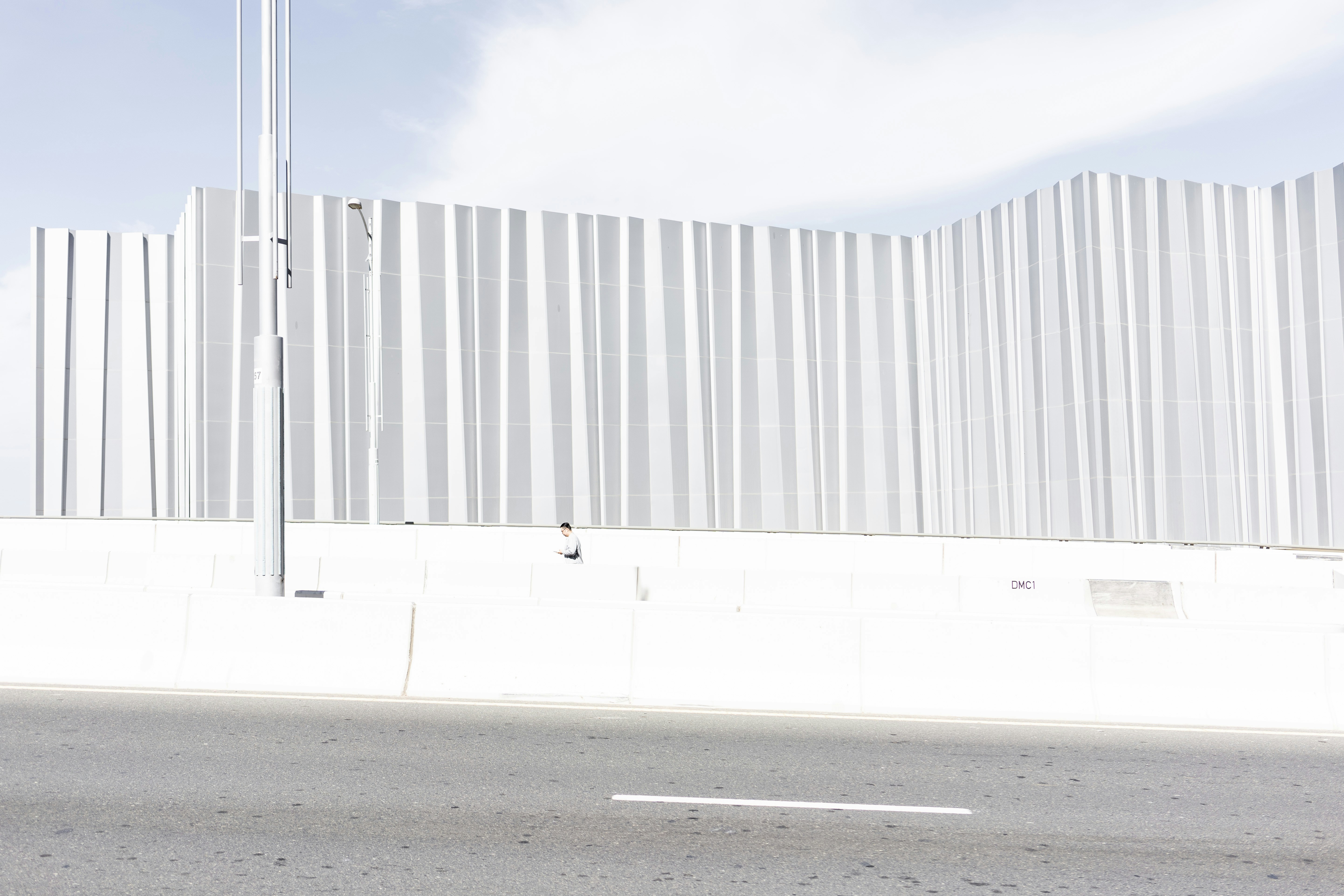 Lone Figure on a Bright Highway Beside a Vertical Barrier