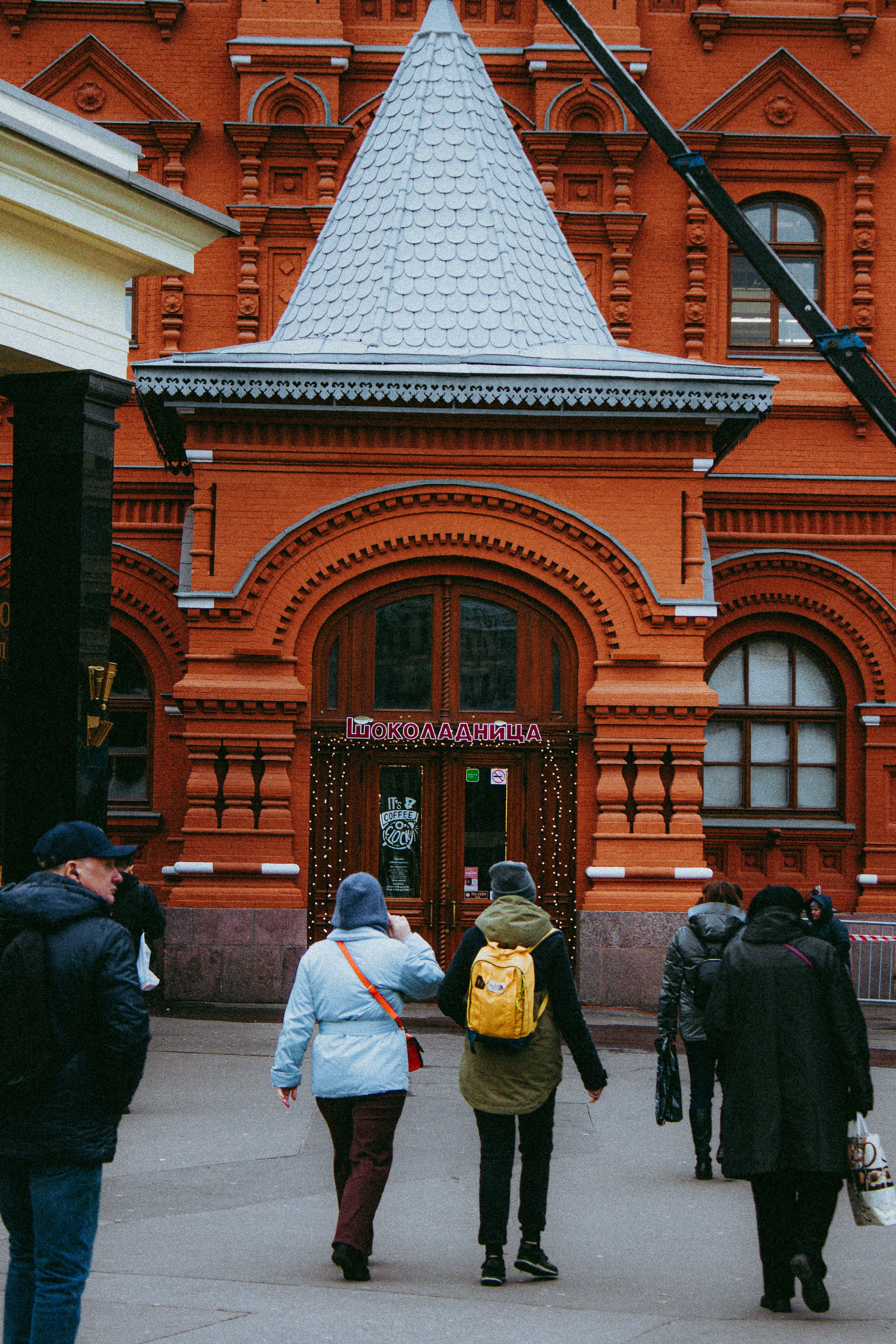 Approaching the Arch: Pedestrians Before a Red-Brick Russian Facade