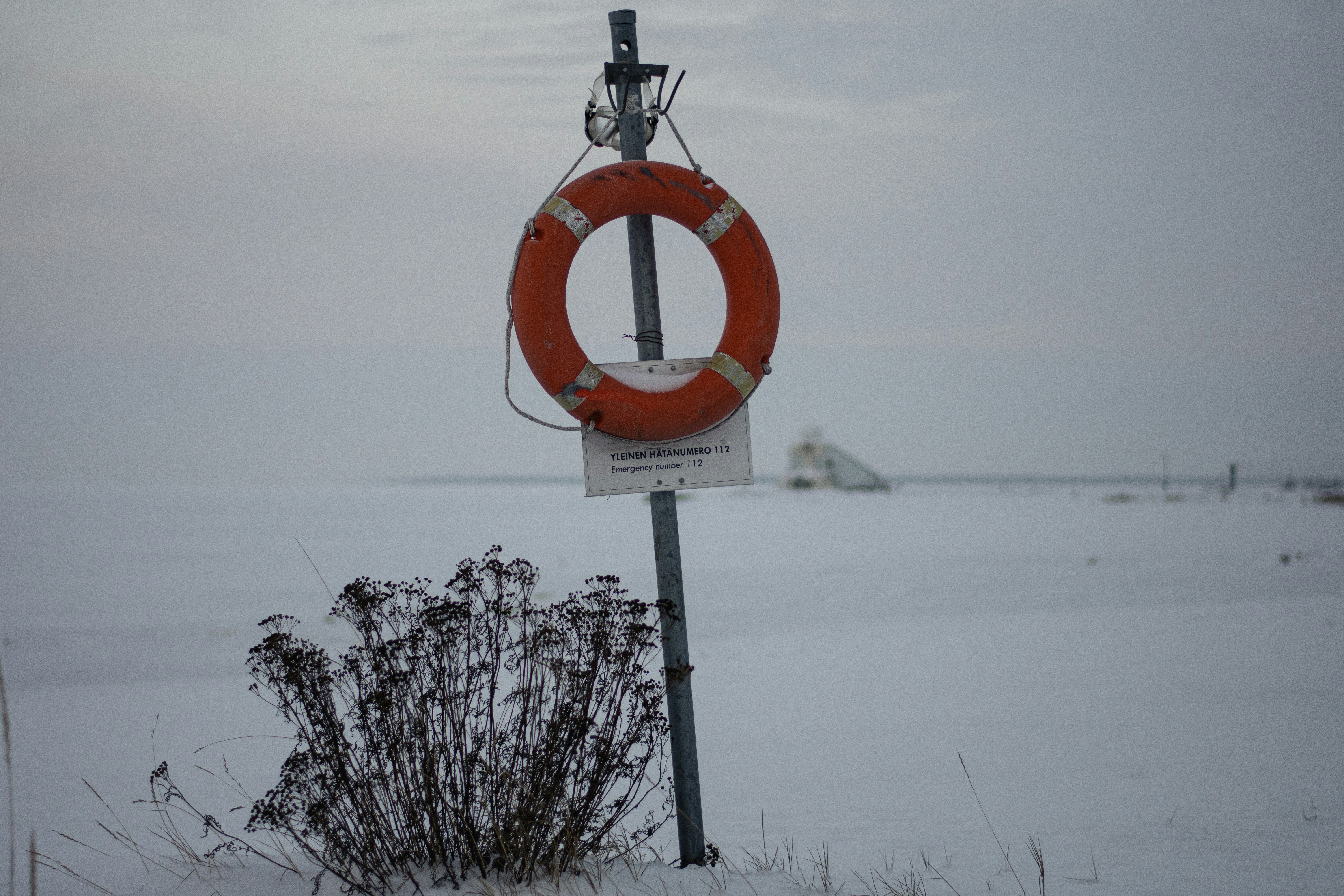 Lifebuoy on a pole amidst a snowy landscape with a distant view of a frozen sea.