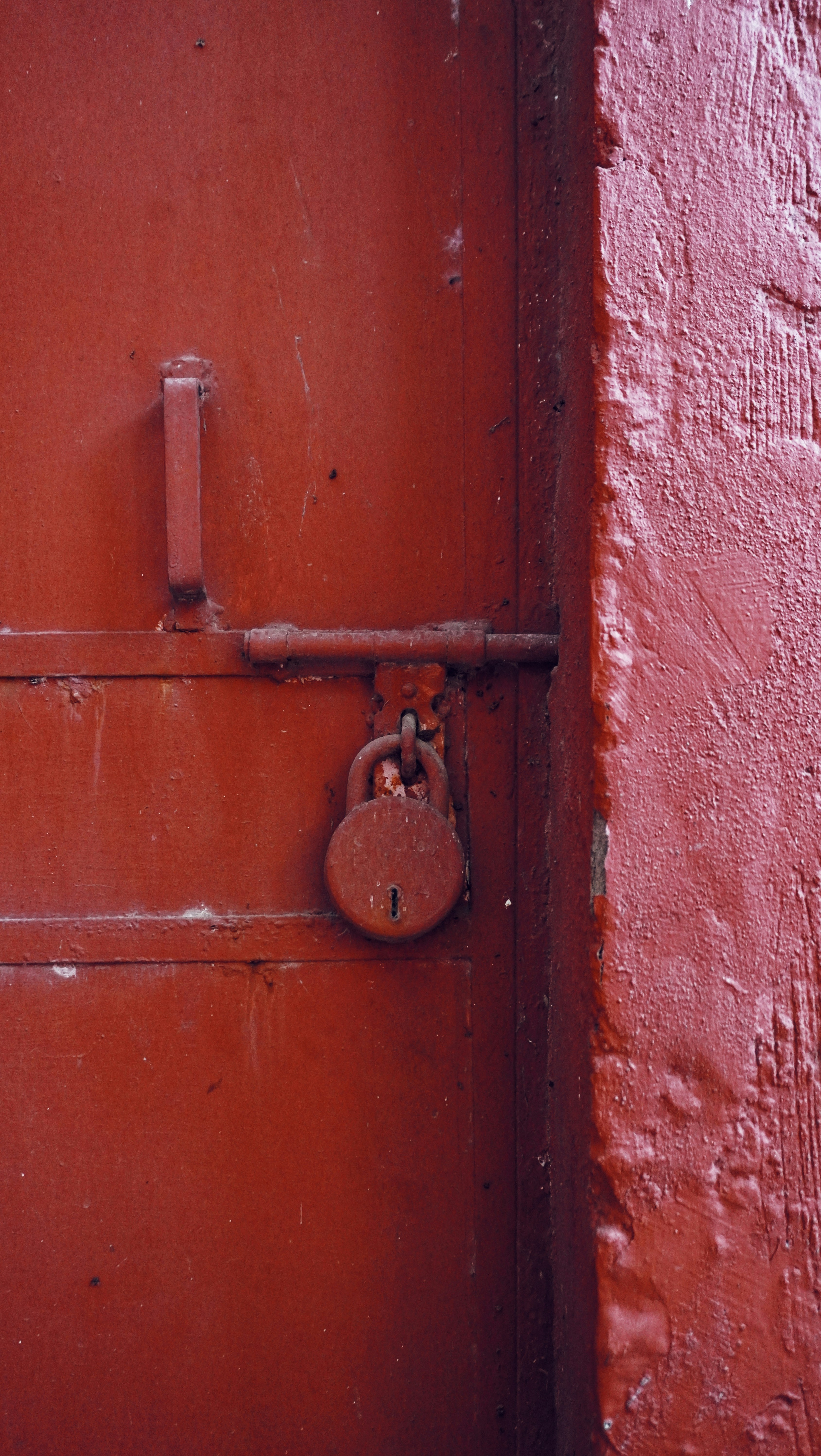 A weathered red door with a rusted padlock, symbolizing security and mystery.