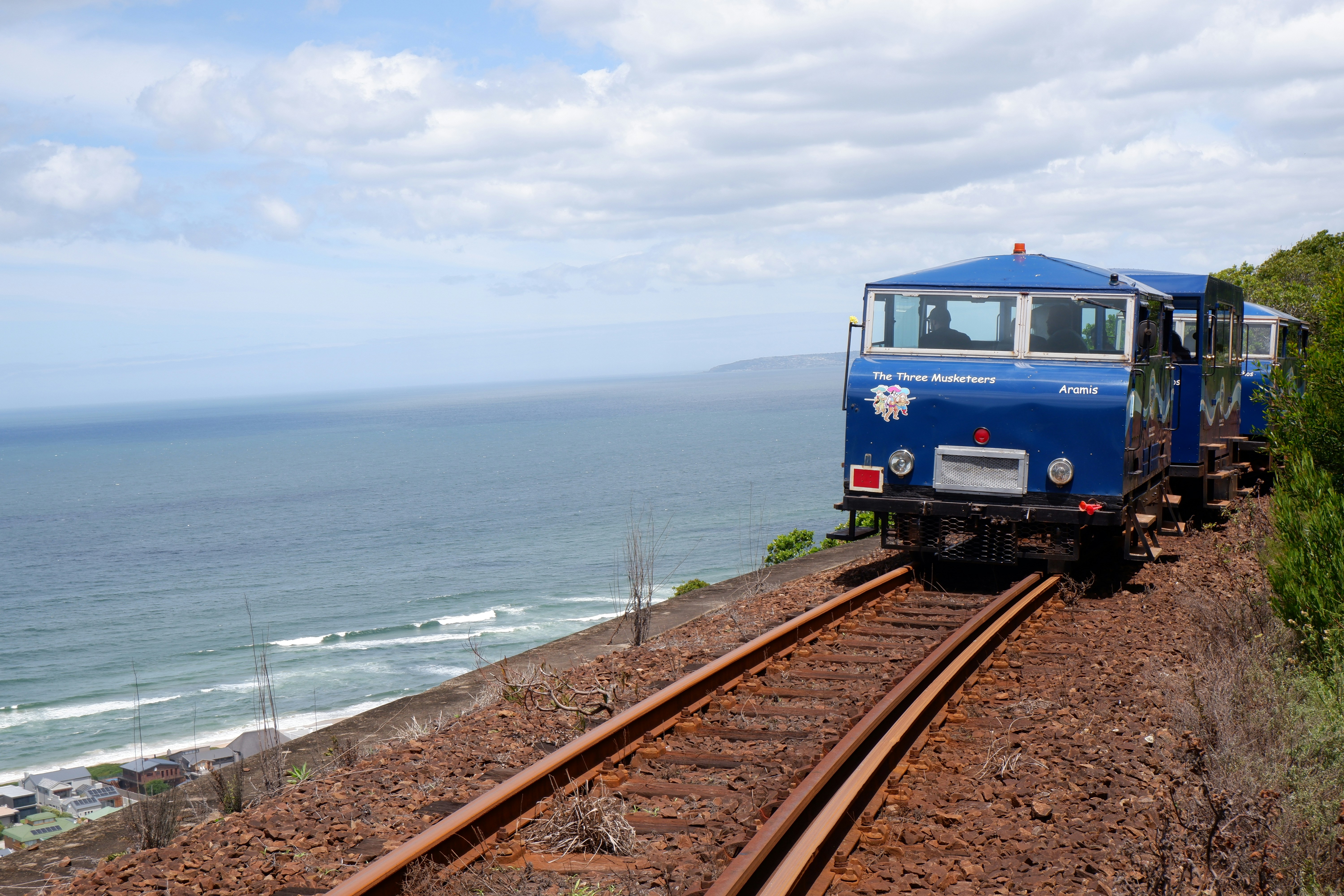 A blue train traveling down train tracks next to the ocean photo – Free ...