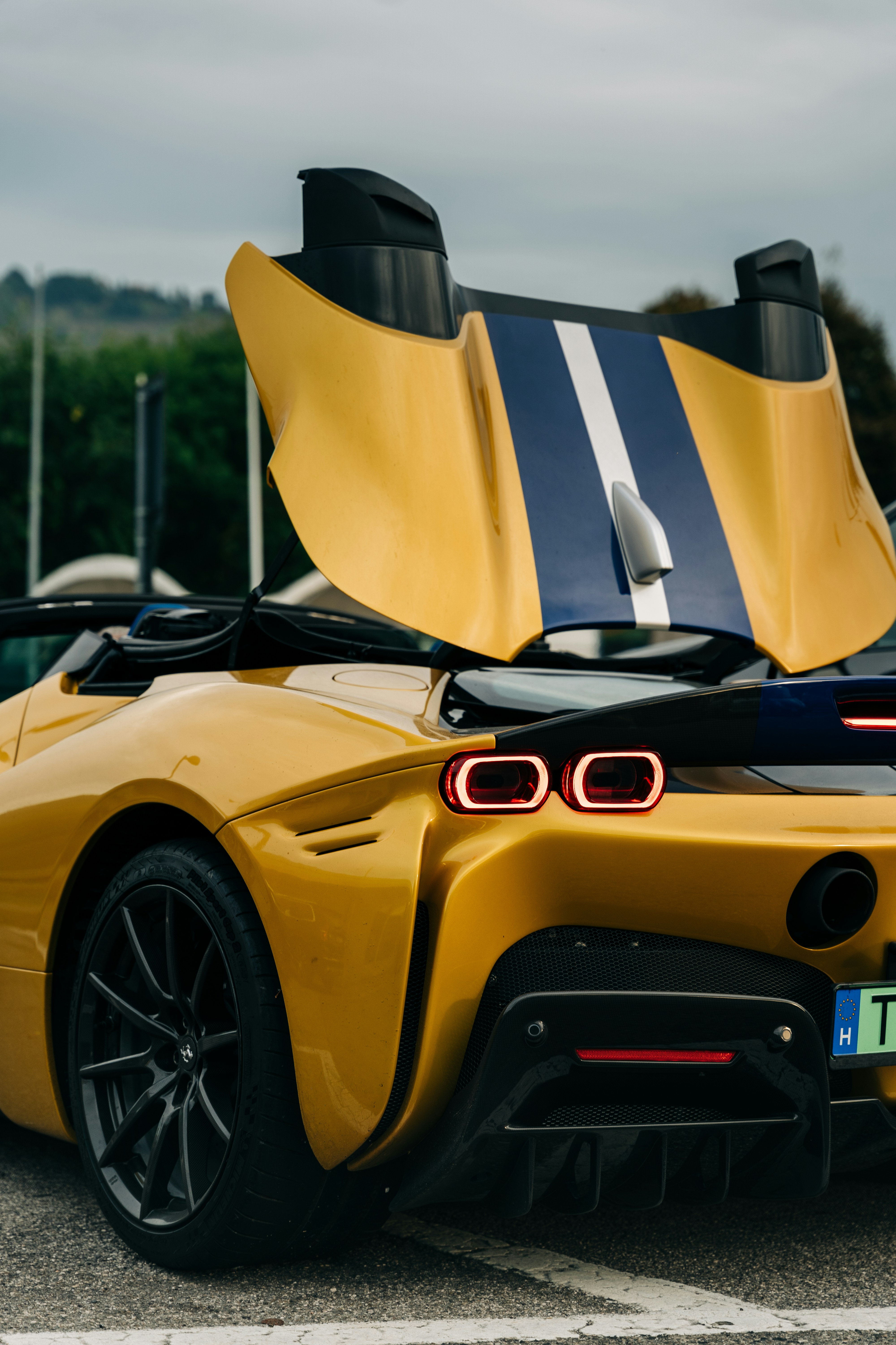 Yellow sports car with striking black and white stripes, featuring open gullwing doors in a parking area.