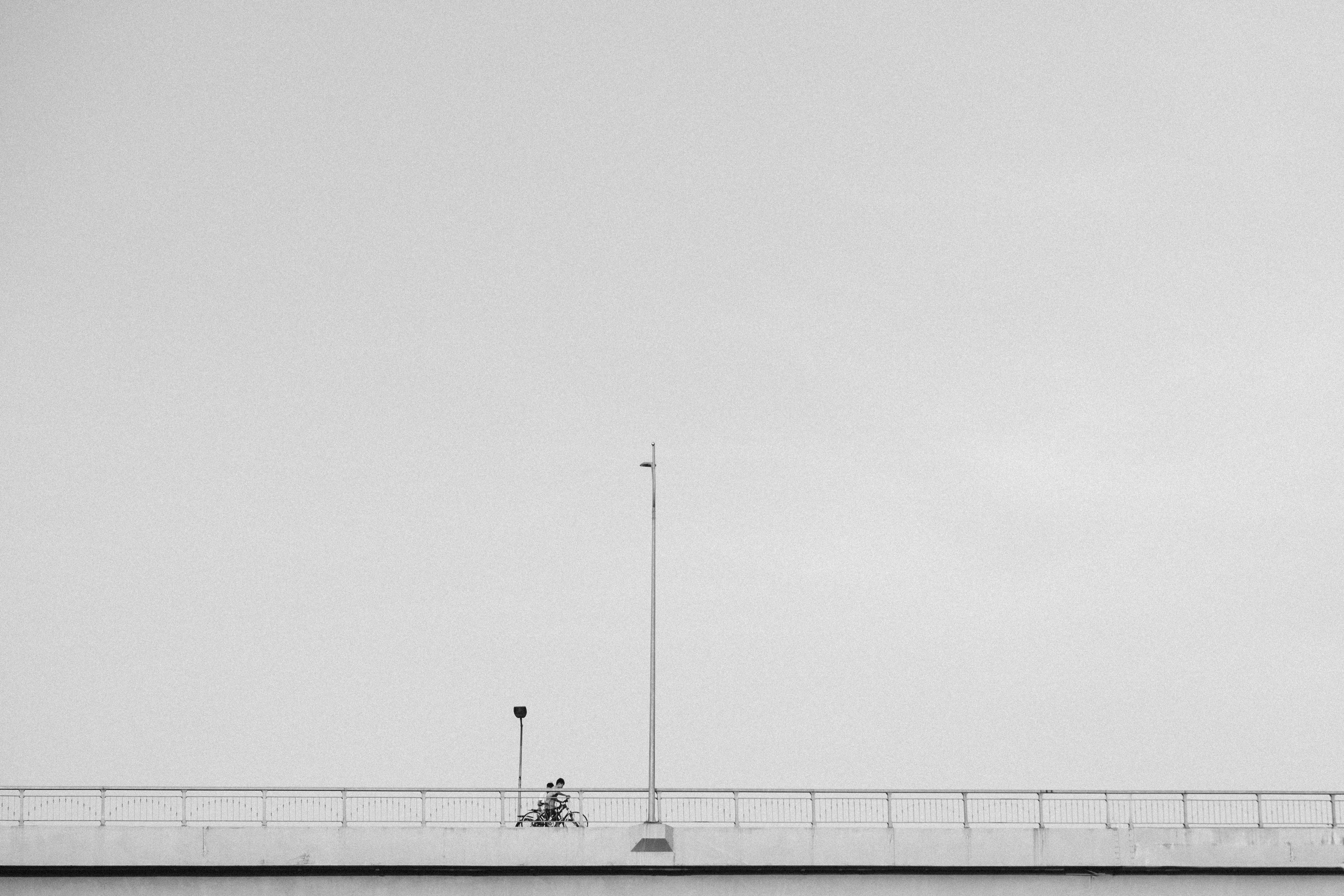 Minimalist scene of a lone street lamp against a vast, overcast sky above a bridge.