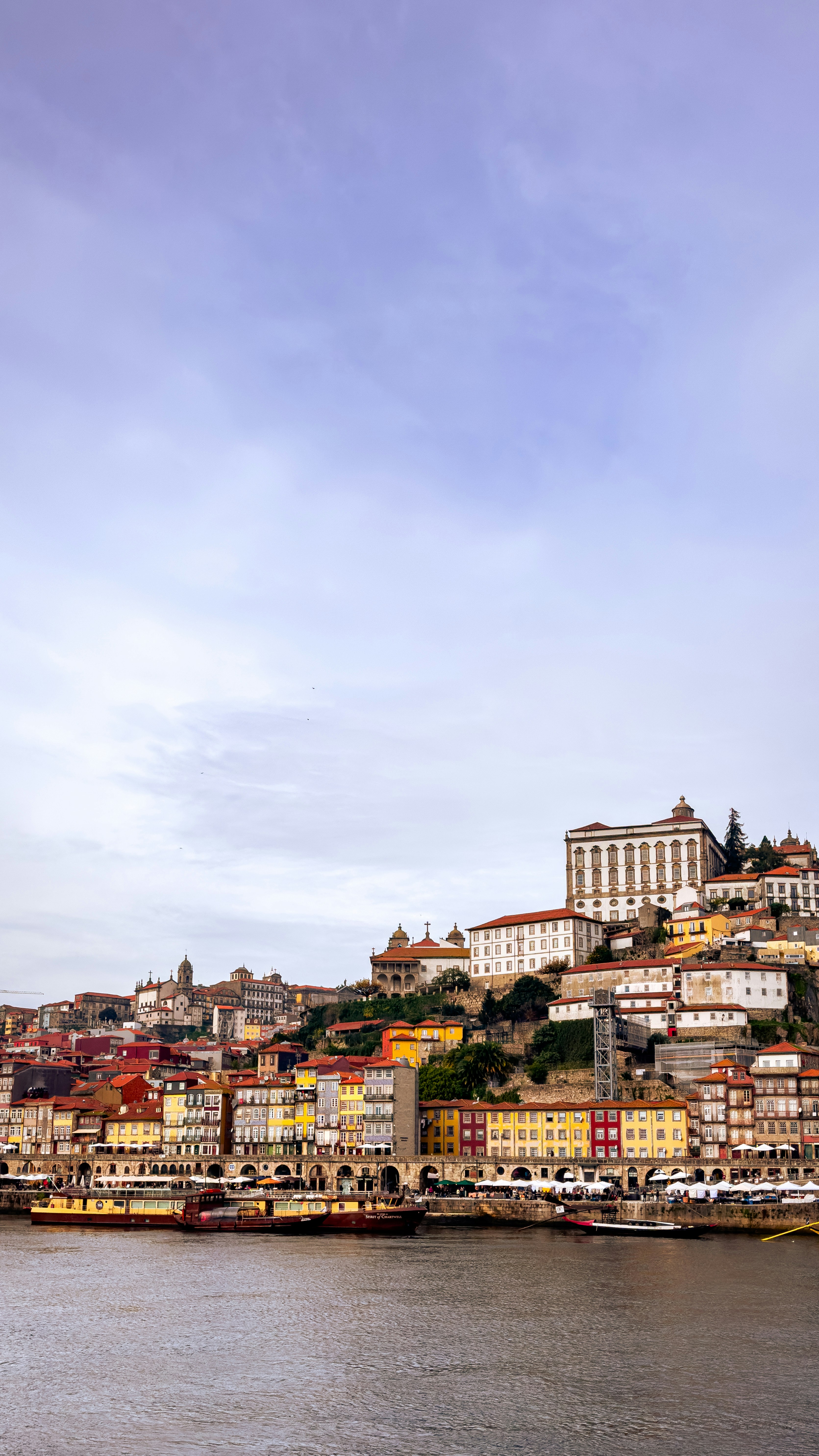 Colorful buildings cascading down a hillside along the Douro River, with a prominent church overlooking the scene.