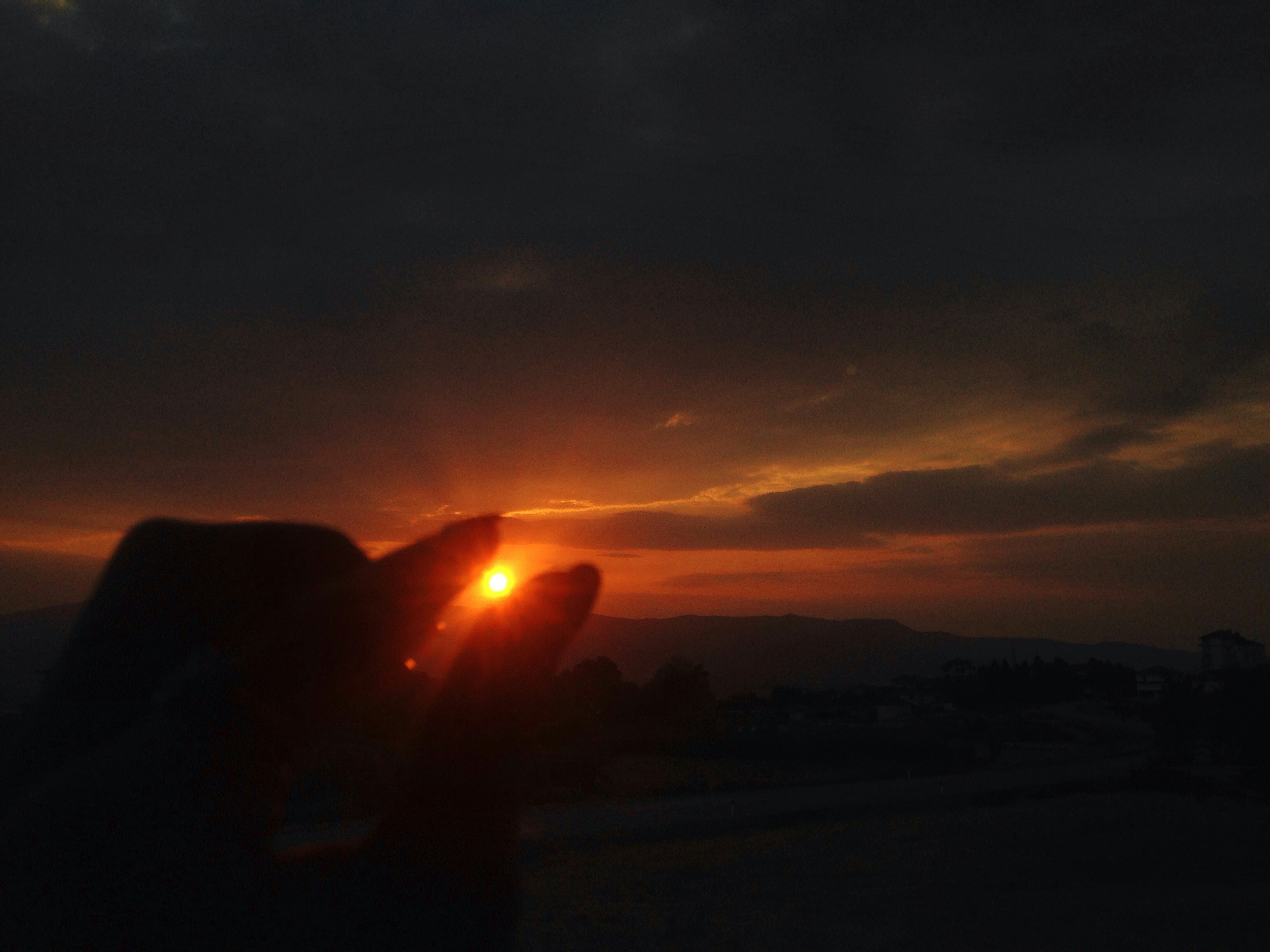 Sun Through Fingers: A Fiery Dusk Over the Distant Horizon