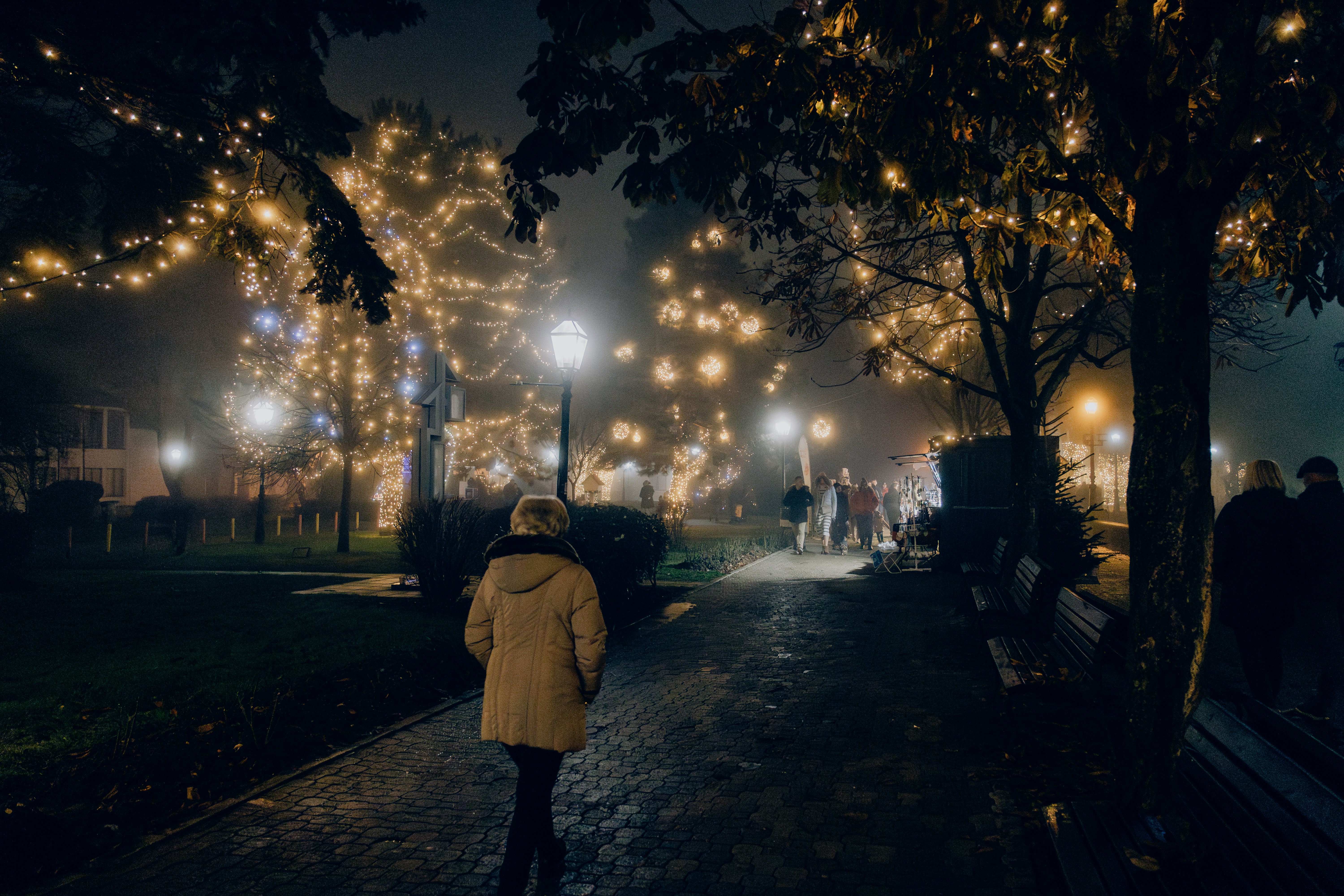 Lantern-lit promenade: a lone figure in a warm coat among glowing winter orbs